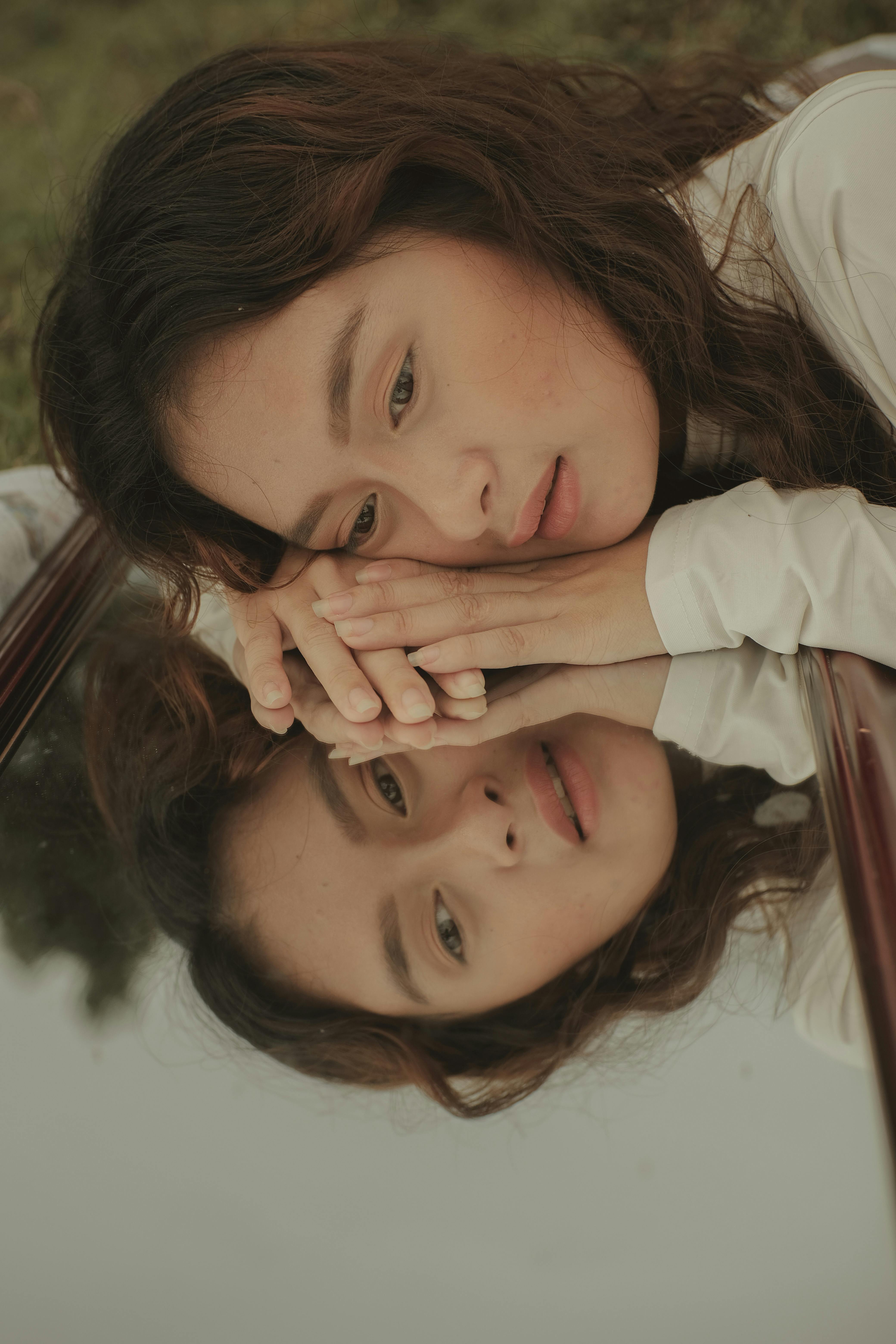 Thoughtful Asian woman lying on car hood with reflection · Free Stock Photo