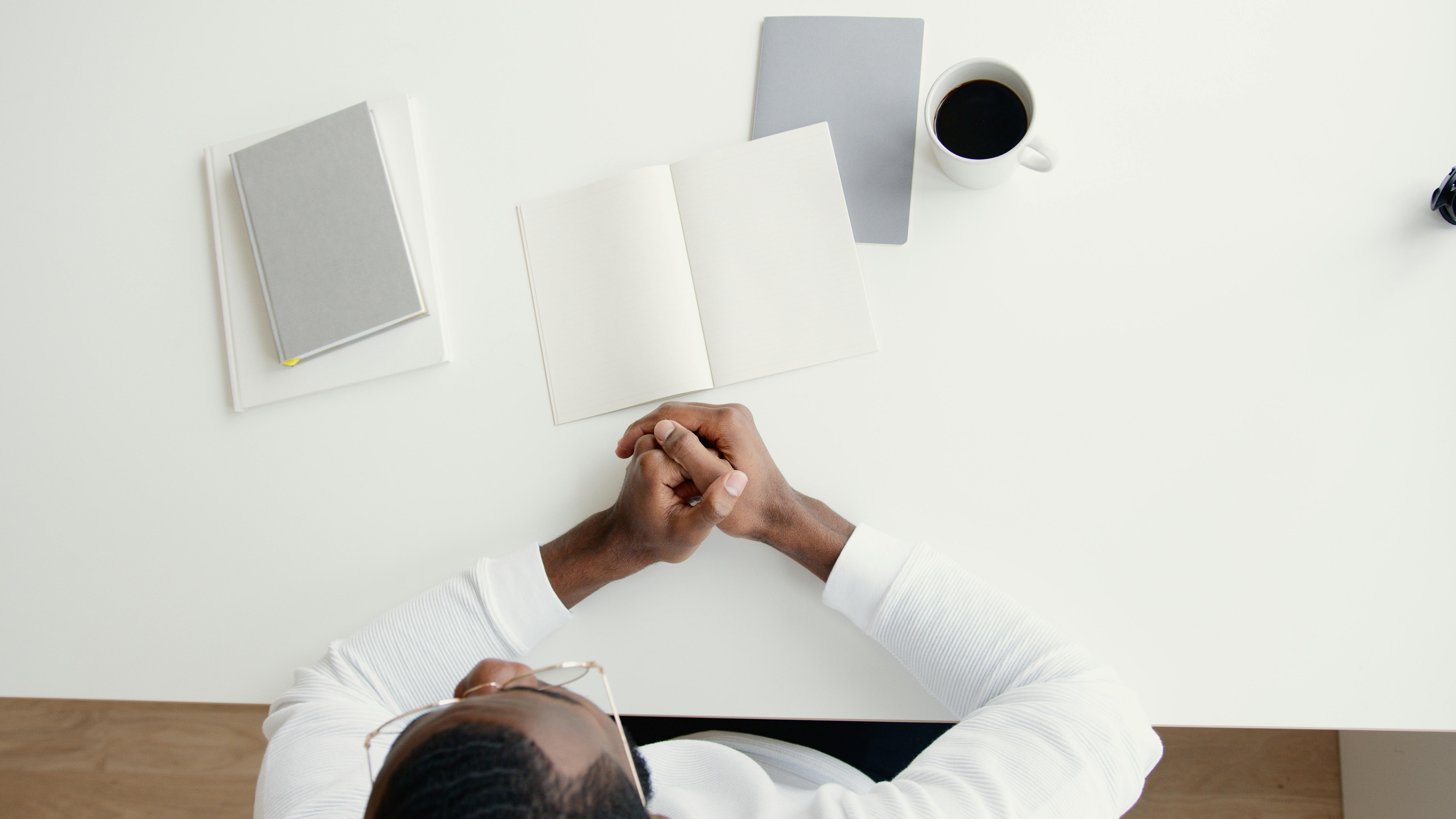 Man Sitting Behind A White Table With White Paper and Notebooks and Cup ...
