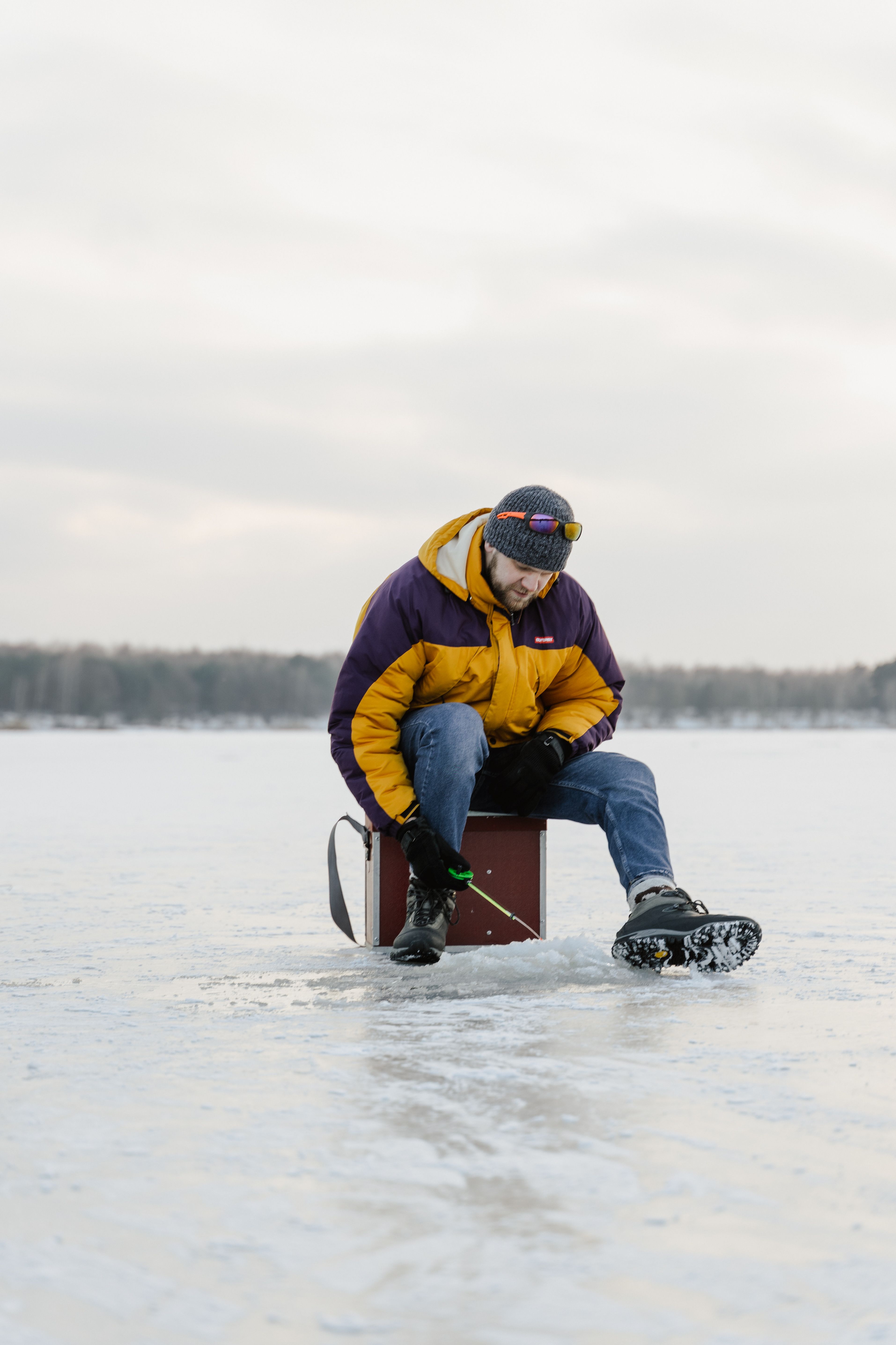 A Man in Blue and Yellow Jacket Fishing on Frozen Lake · Free Stock Photo