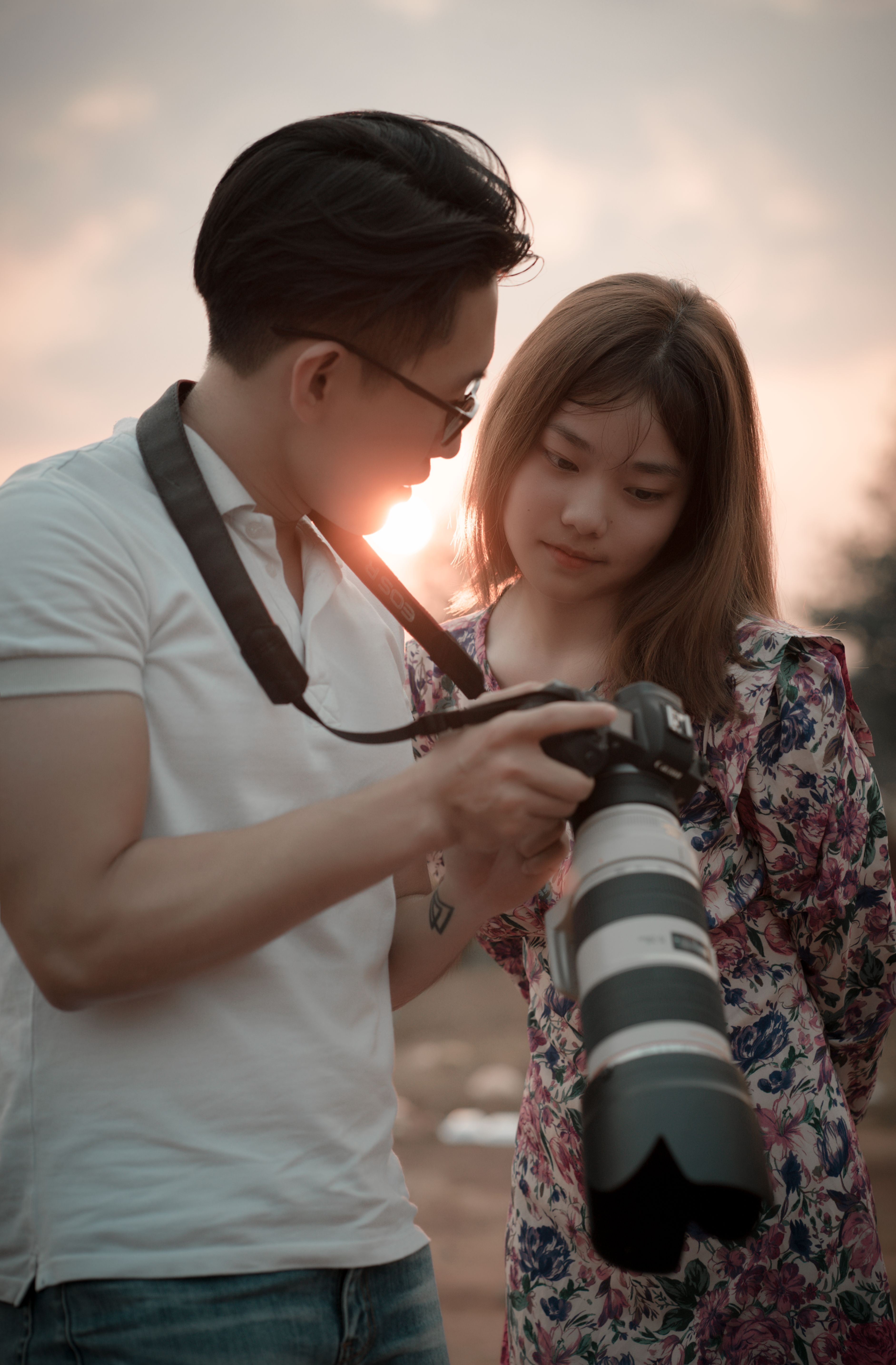 Man in White T-shirt Showing Photos on Camera to Woman in Floral Dress ...