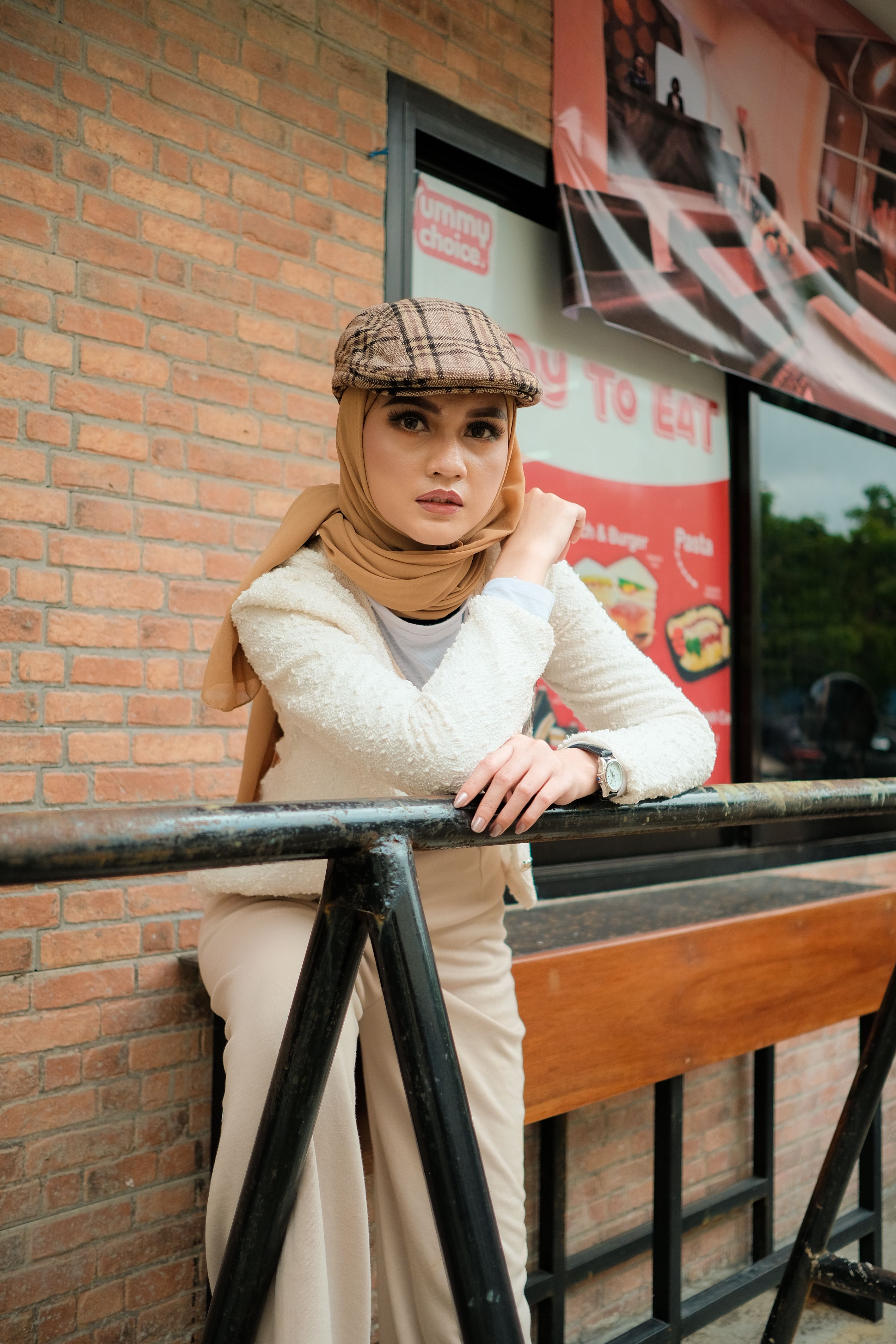 A Woman in Hijab and Beret Hat Leaning on a Brick Wall while Looking ...