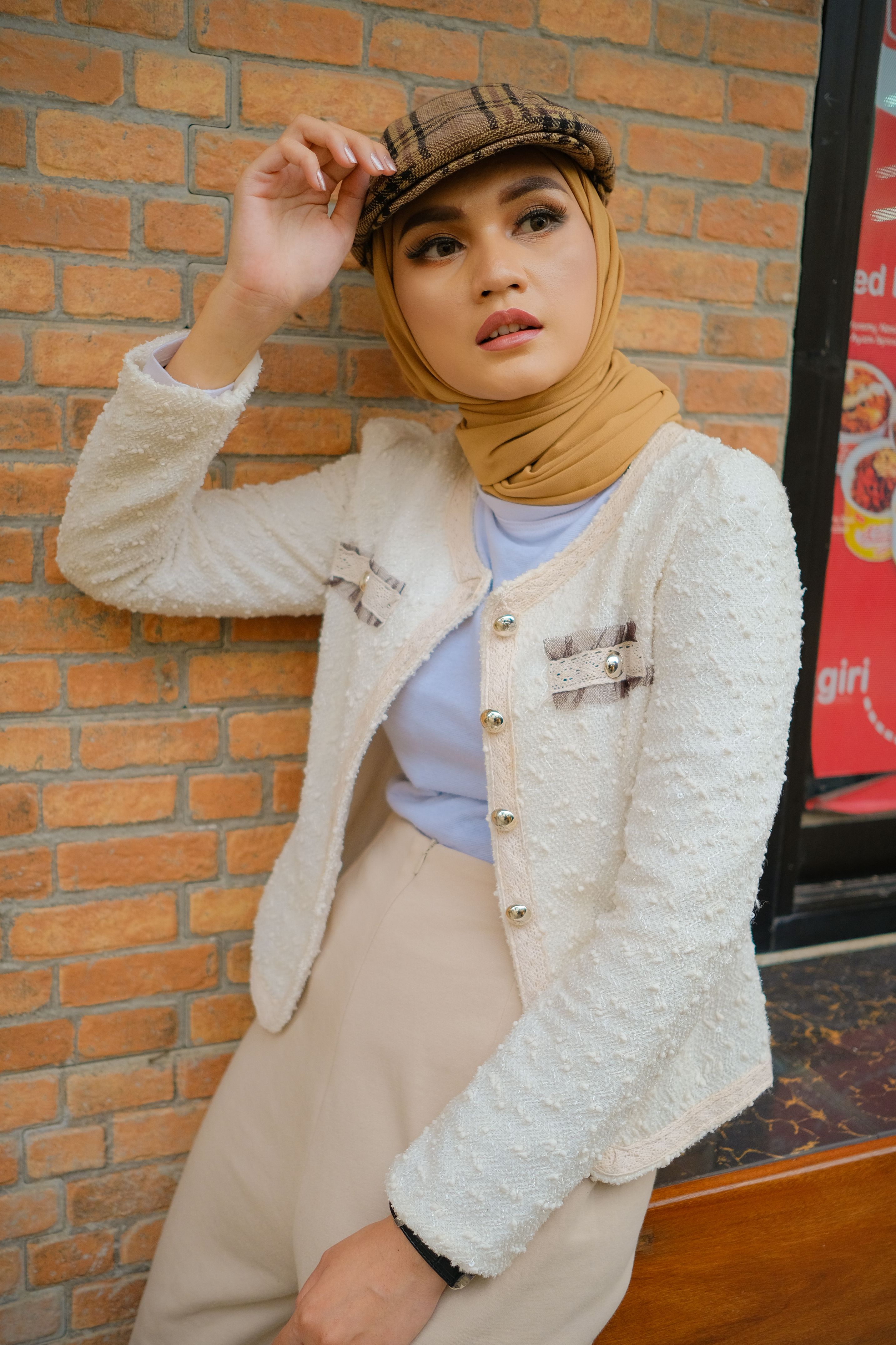 A Woman in Hijab and Beret Hat Leaning on a Brick Wall while Looking ...
