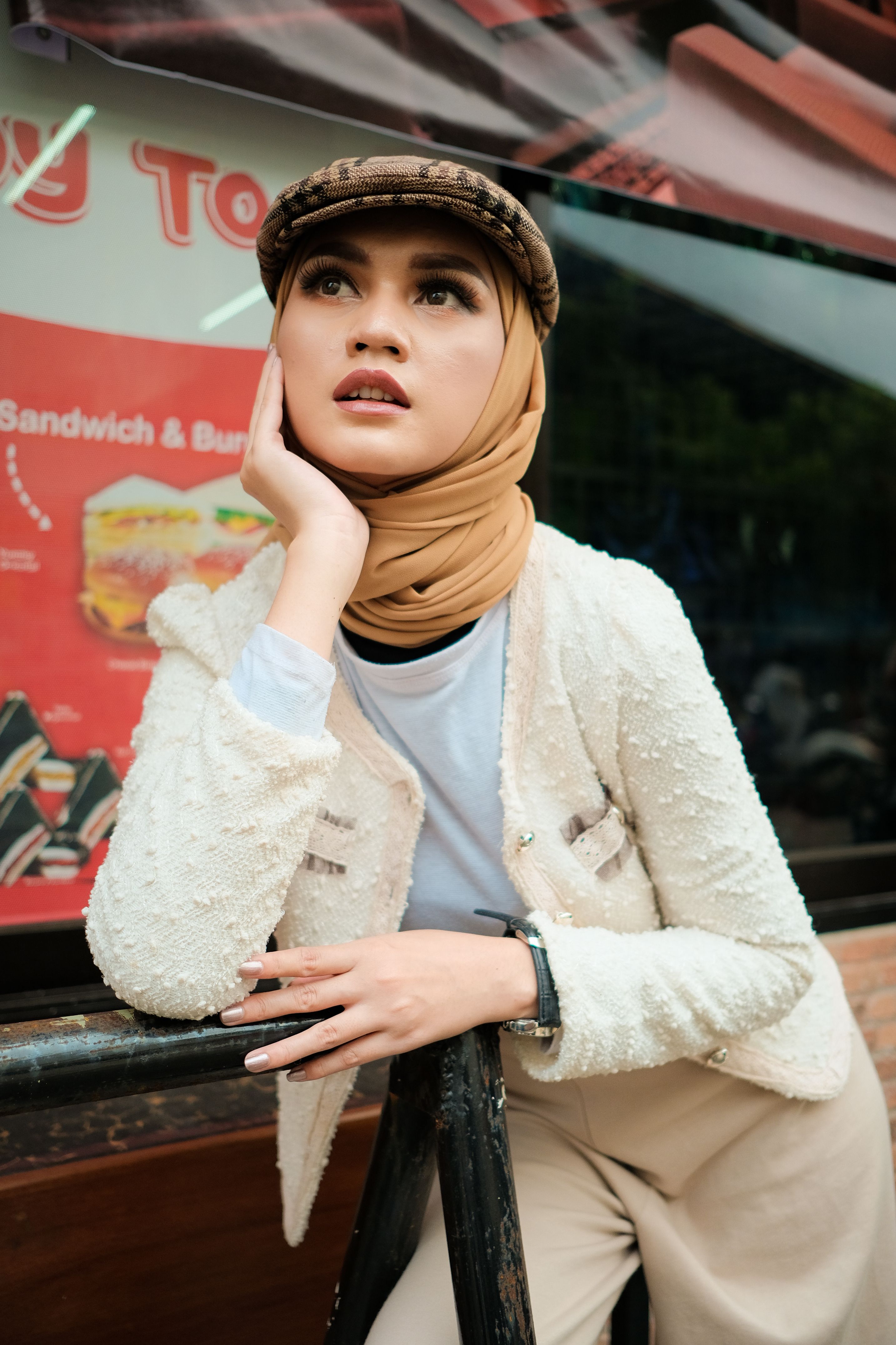 A Woman in Hijab and Beret Hat Leaning on a Brick Wall while Looking ...