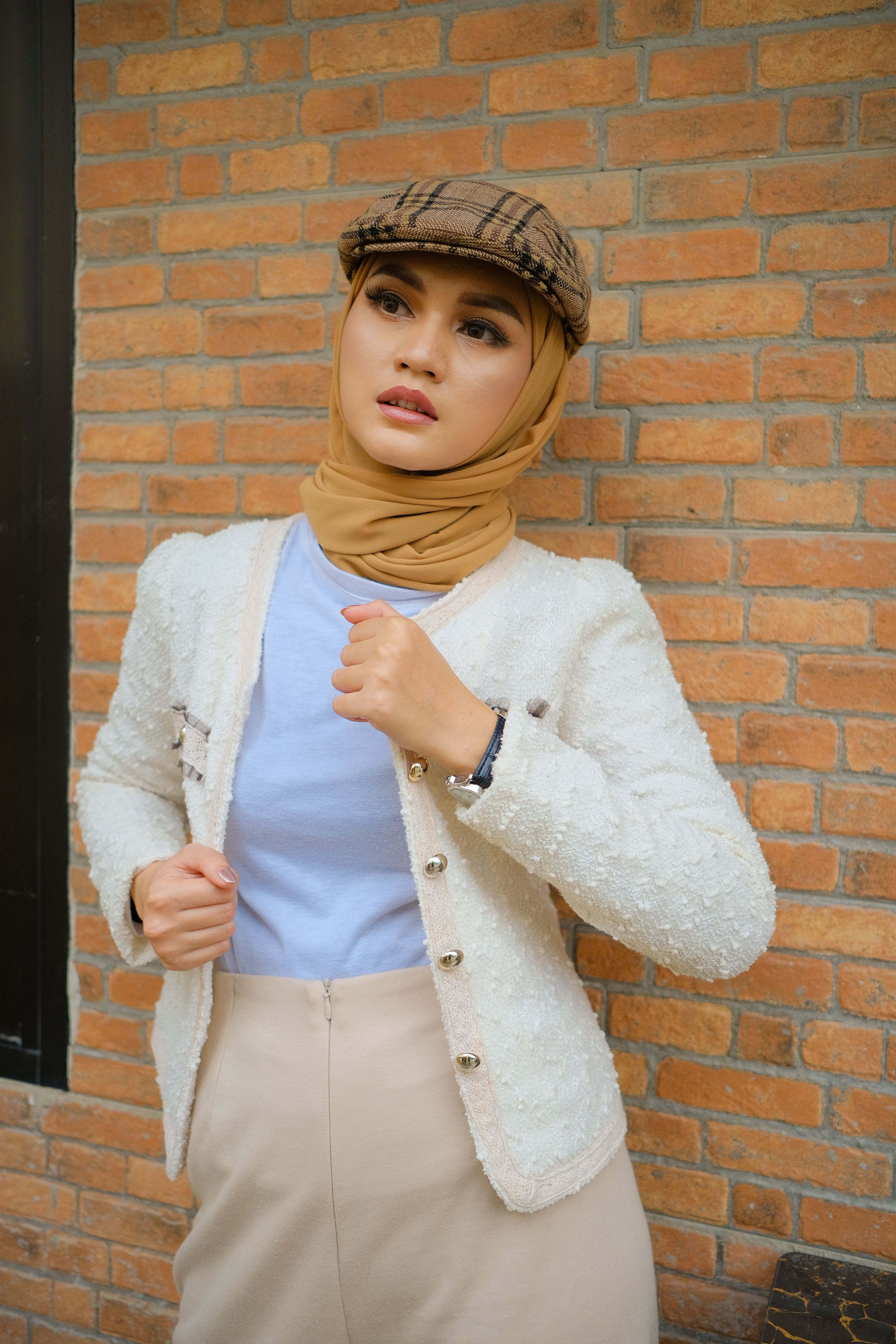 A Woman in Hijab and Beret Hat Leaning on a Brick Wall while Looking ...