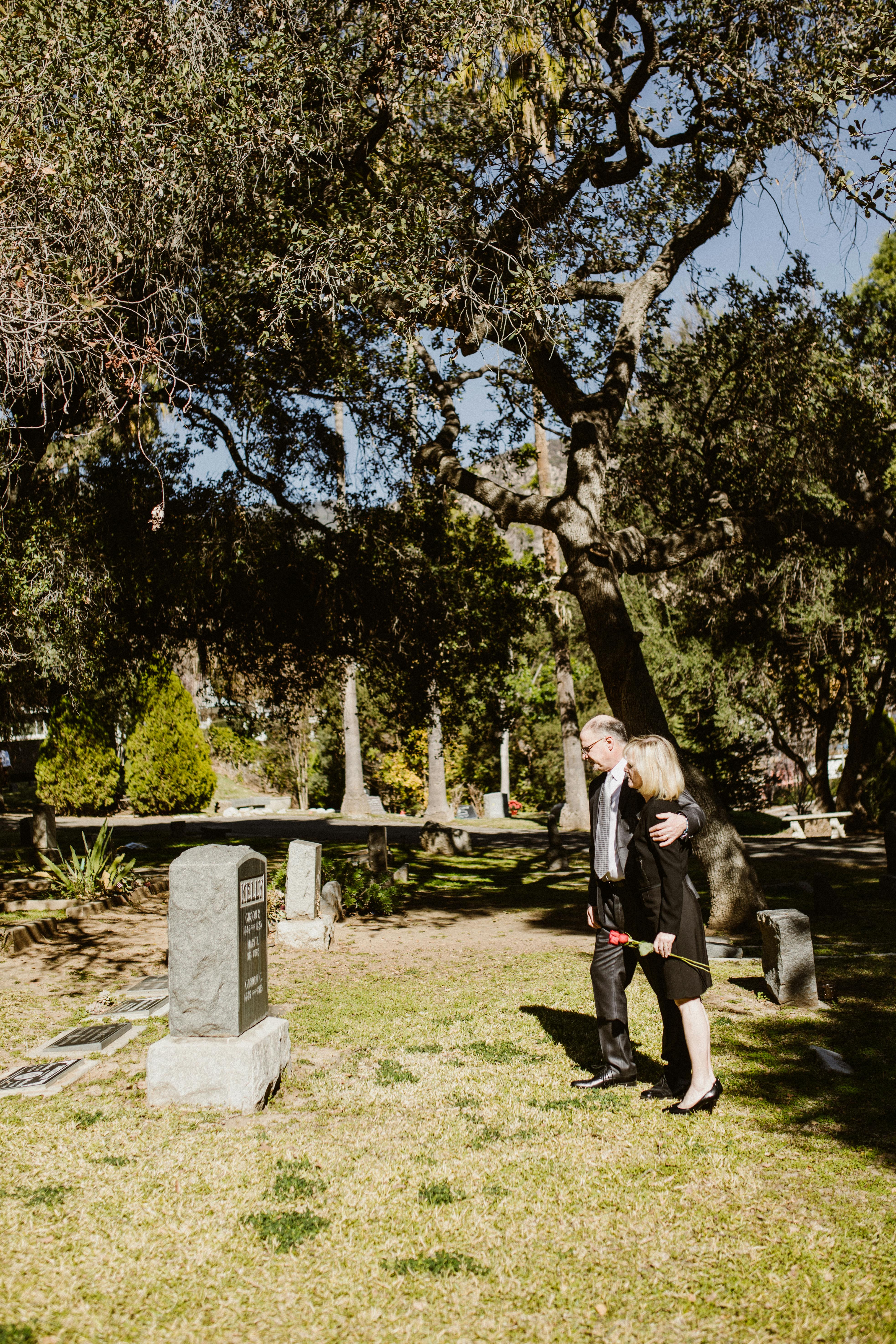 A Couple Embracing while Standing In Front of a Gravestone · Free Stock ...