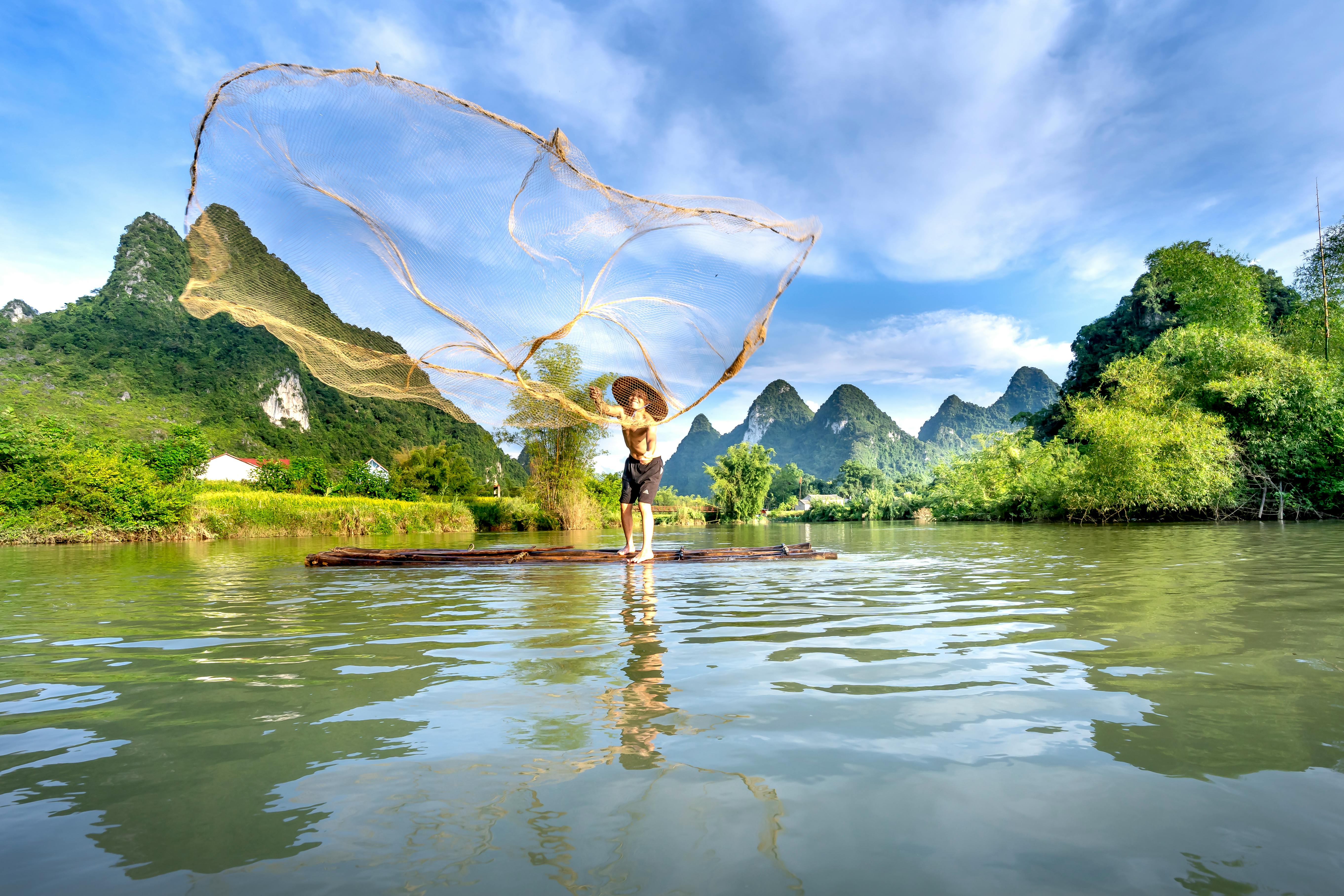 Man Throwing a Fishing Net While Standing on a Raft · Free Stock Photo