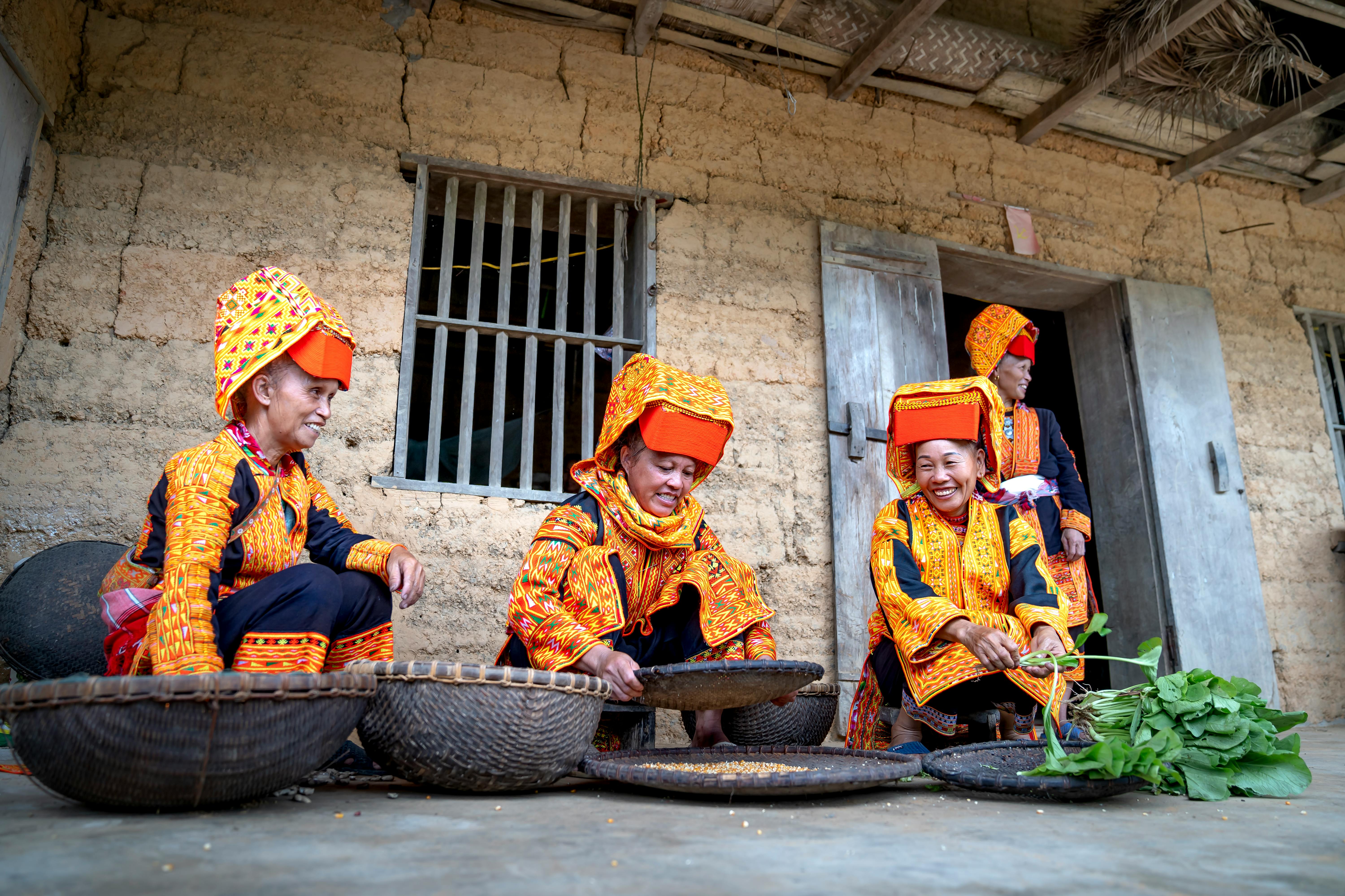 Women in Orange Traditional Clothes Working Outside a Rough Beige House ...