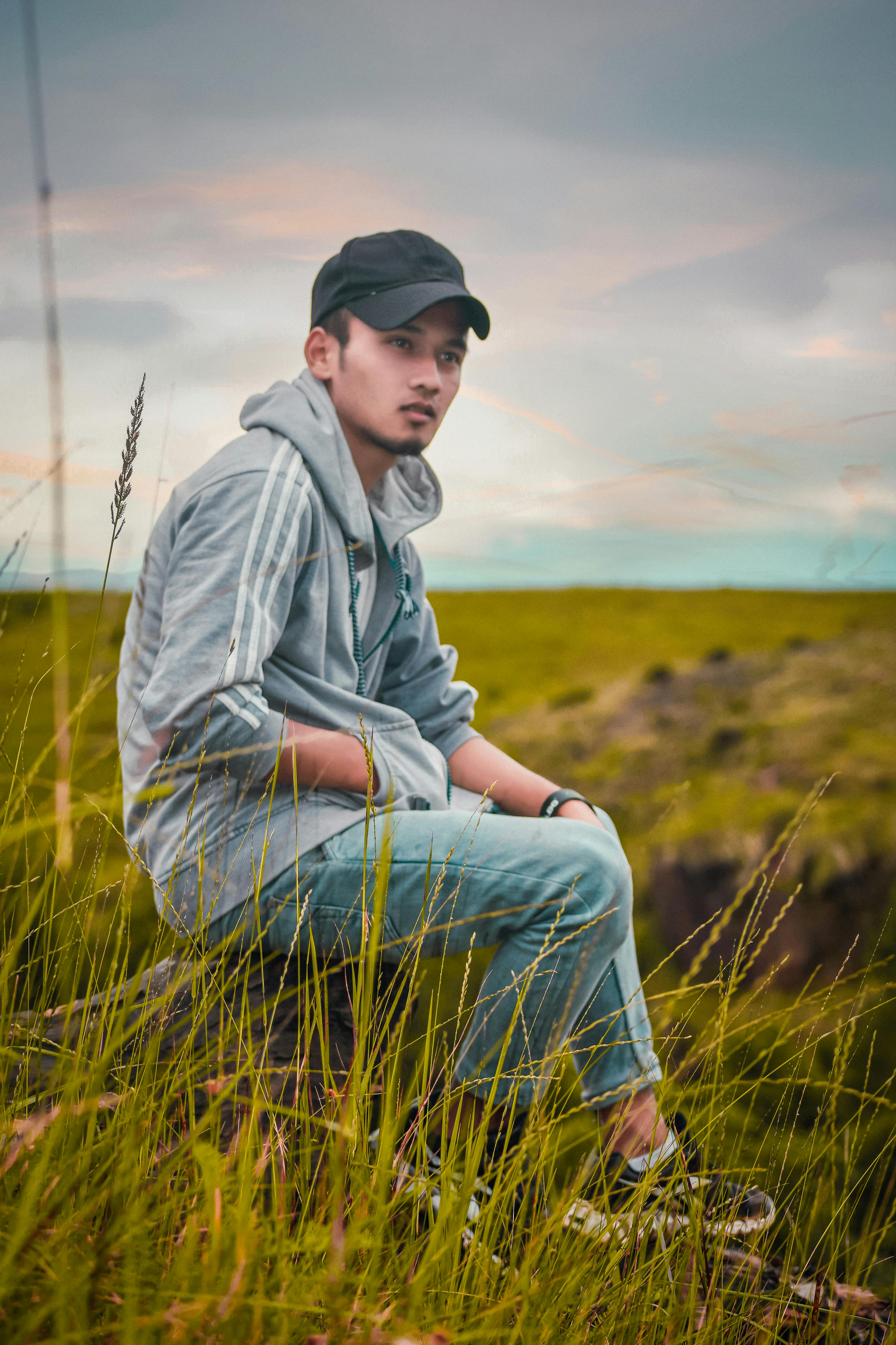 Young Man in Casual Clothing and a Baseball Cap Sitting on a Field ...