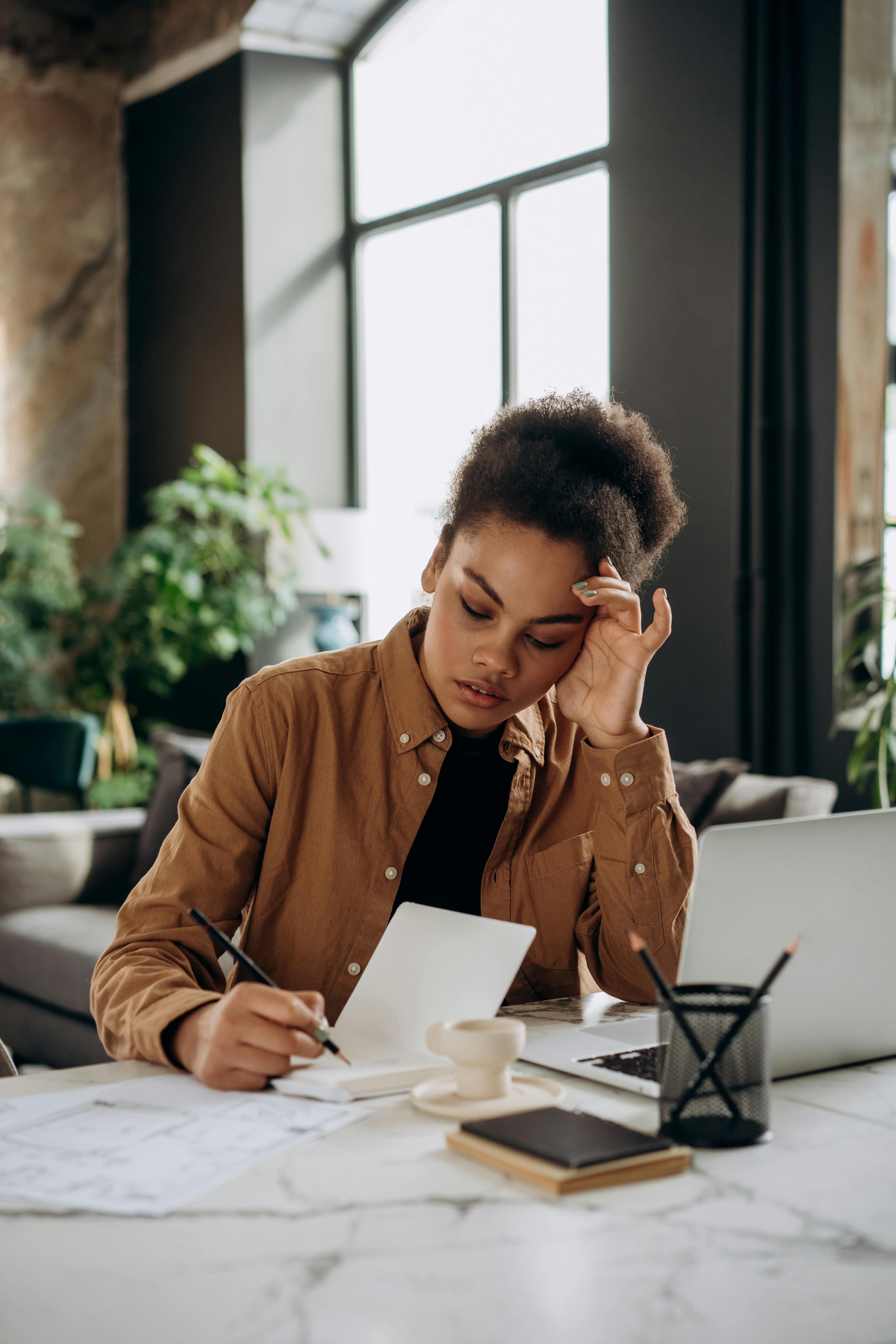 Woman Holding her Head While Writing · Free Stock Photo