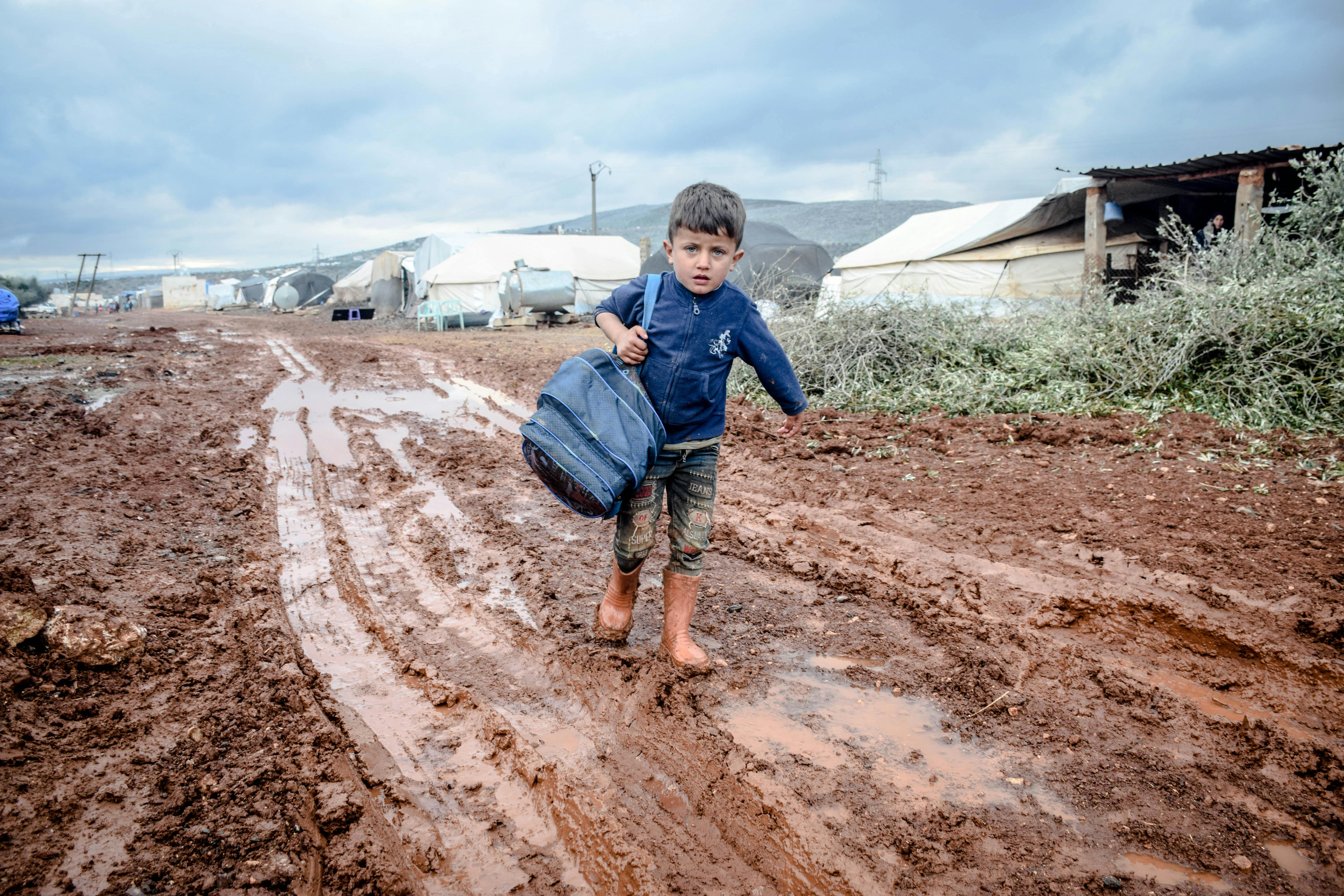 Little boy carrying backpack on dirty road · Free Stock Photo