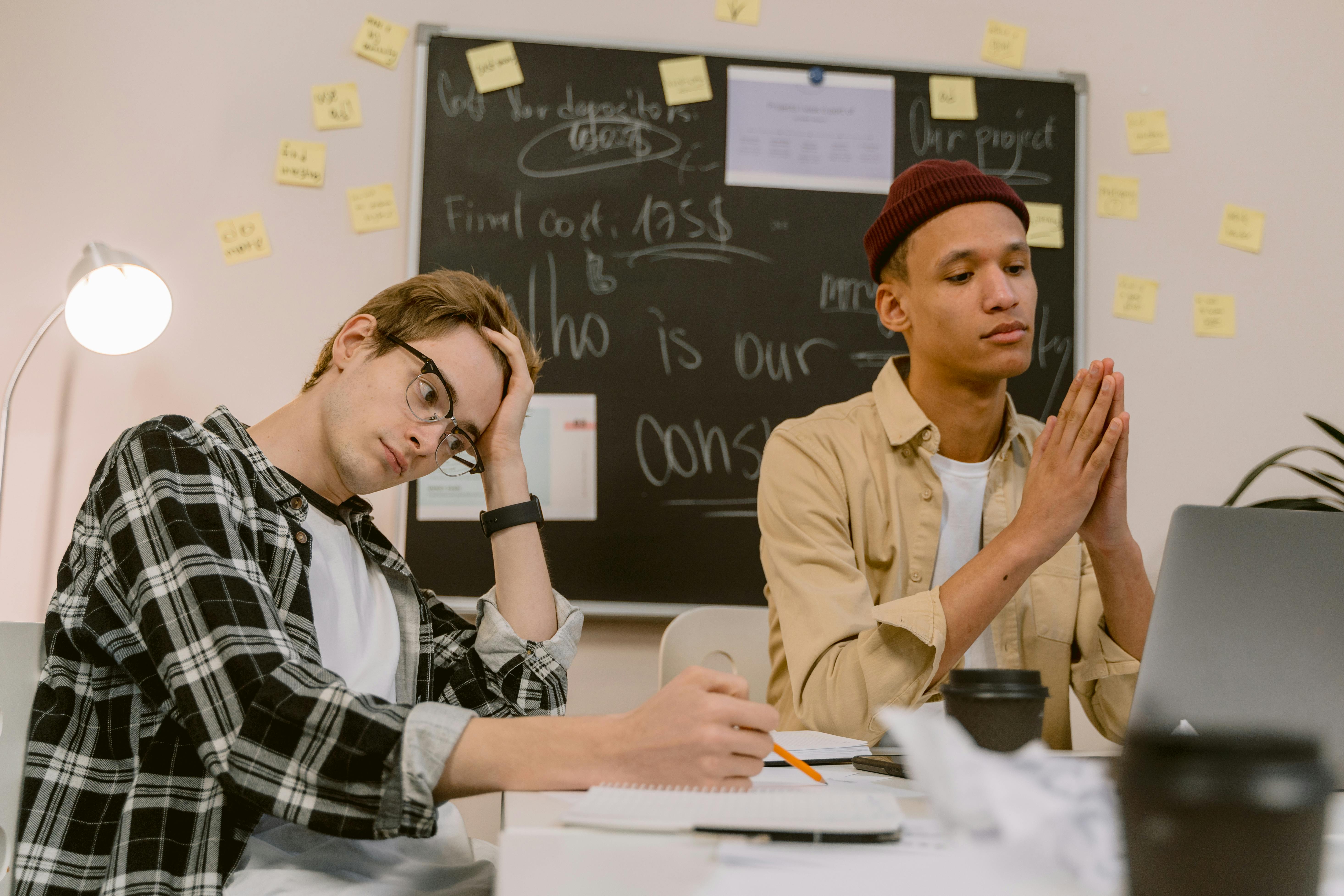 Two Men Sitting at a Table Near a Blackboard · Free Stock Photo