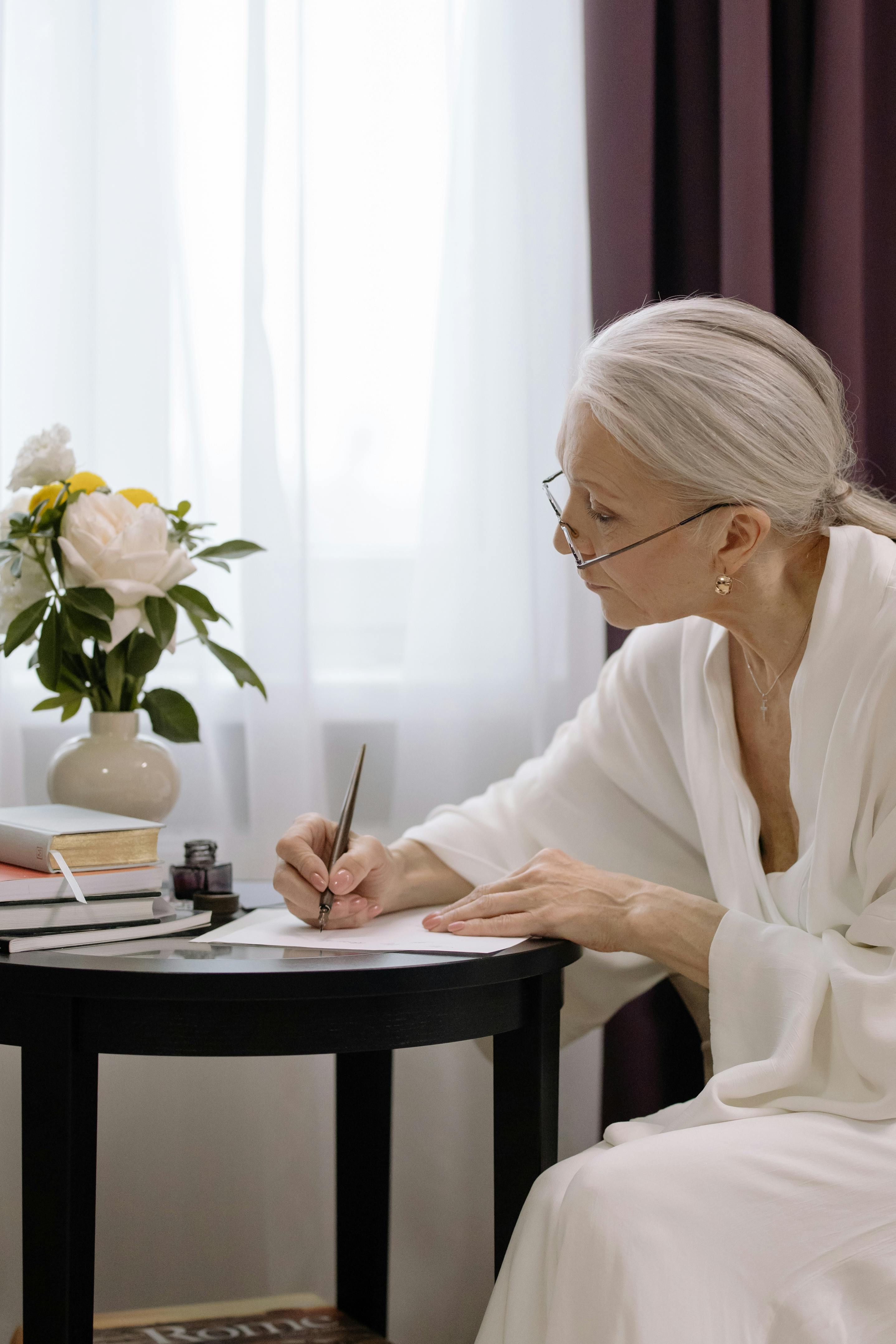 A Woman in White Robe Writing on the Table · Free Stock Photo