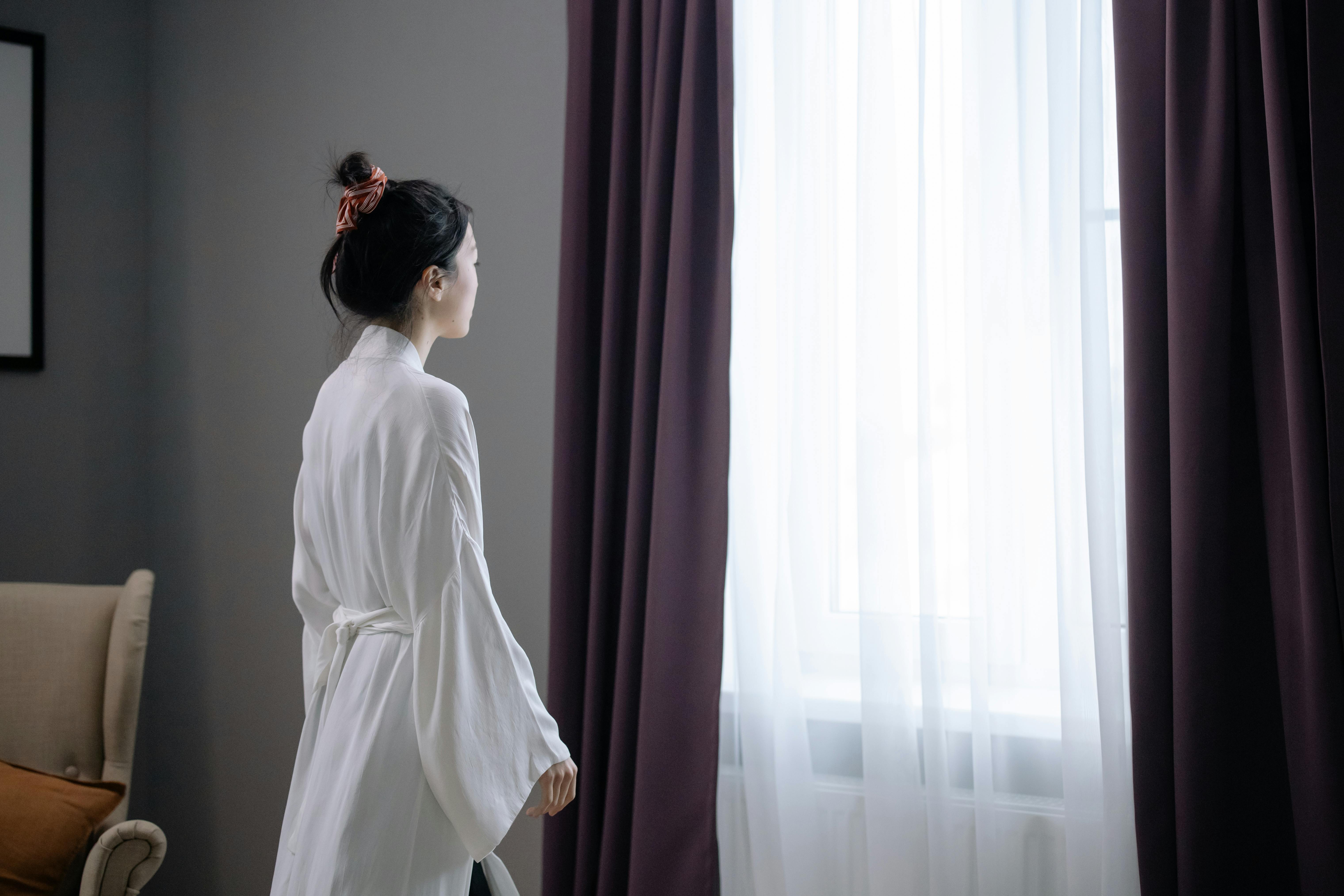 A Woman in White Robe Standing Beside Sheer Curtain · Free Stock Photo