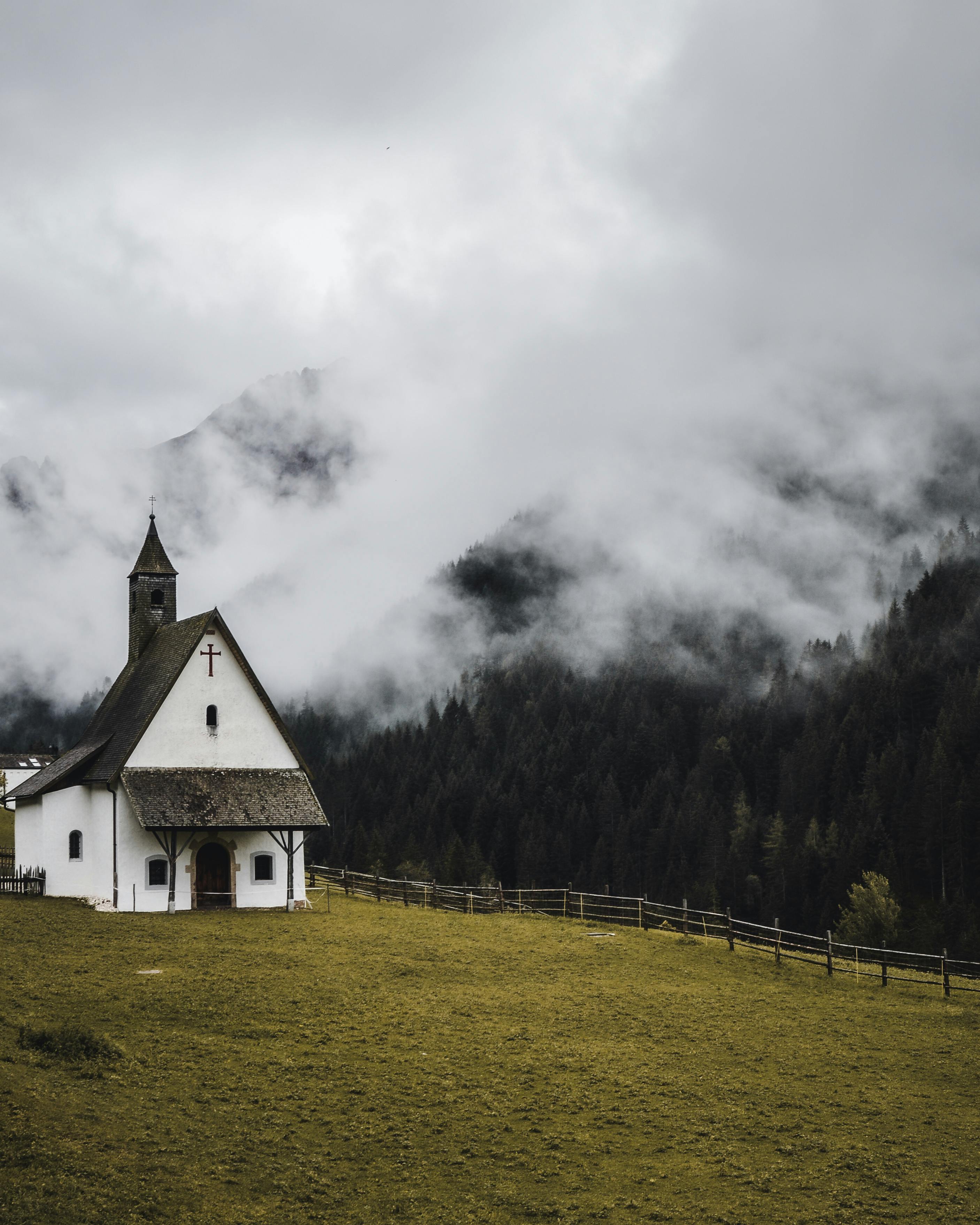 Small church near grassy lawn and green hills under fog · Free Stock Photo