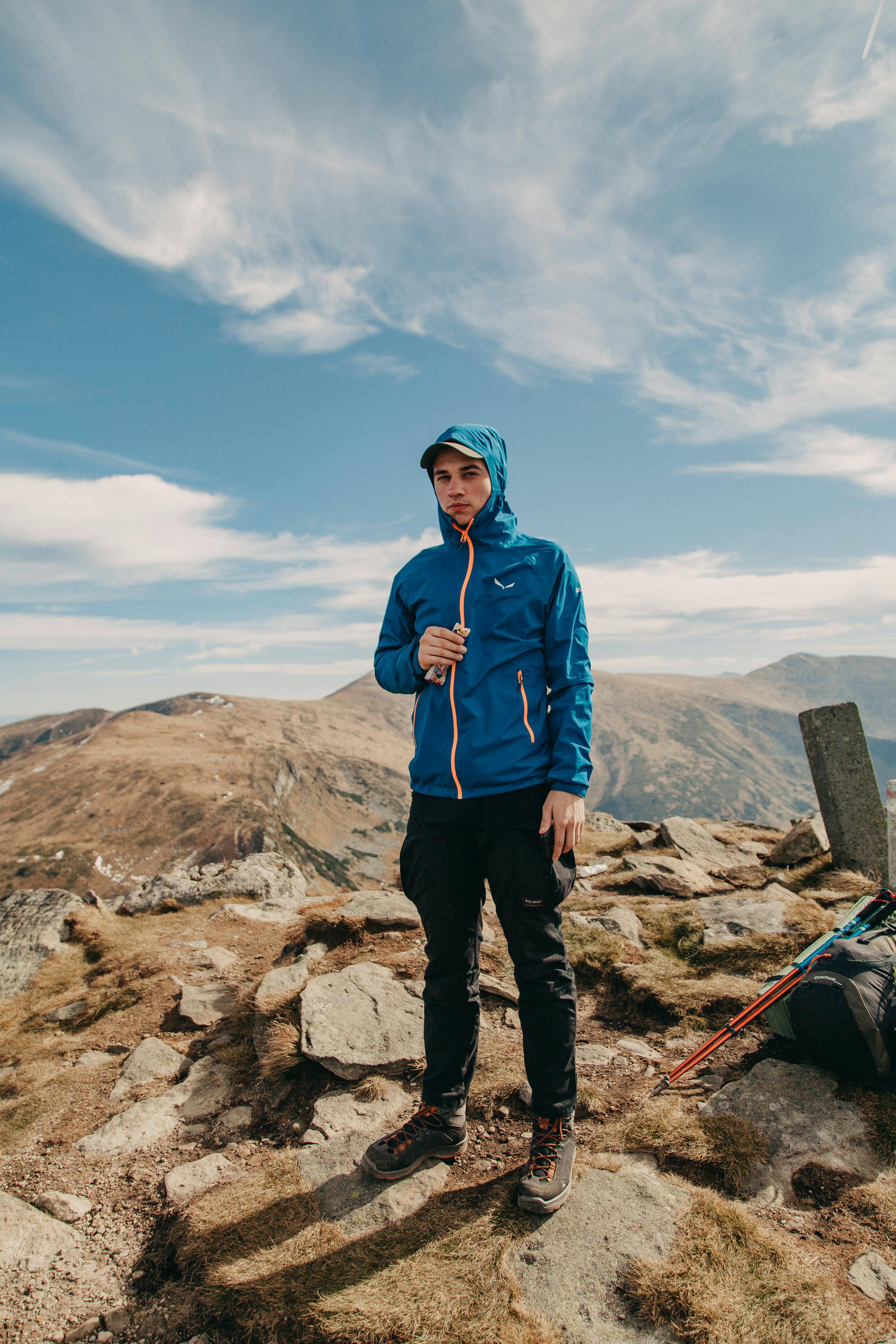 Man in Blue Hoodie Standing on a Rocky Mountain while Looking at the ...