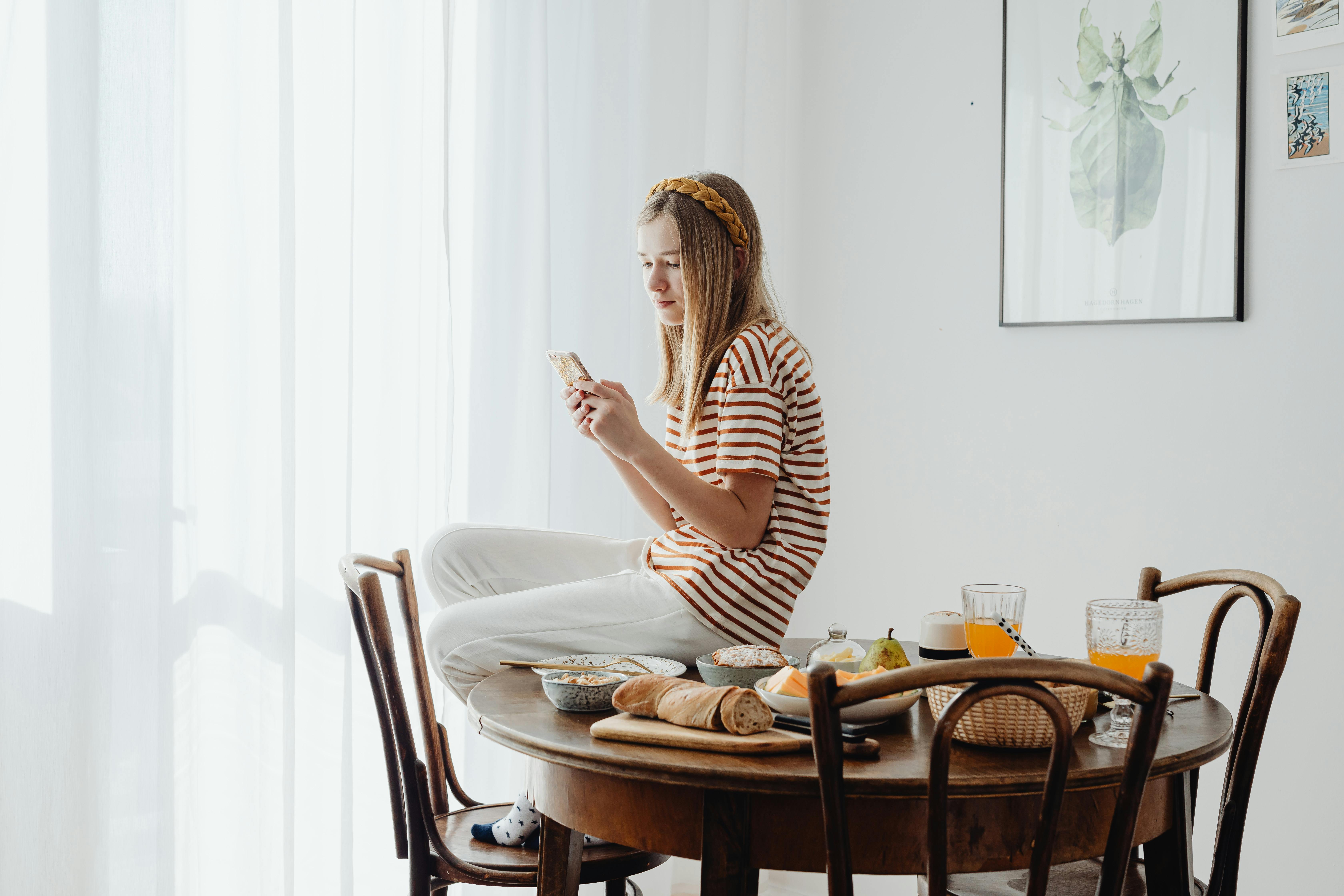 A Woman Sitting on a Wooden Table while Using Her Mobile Phone · Free ...