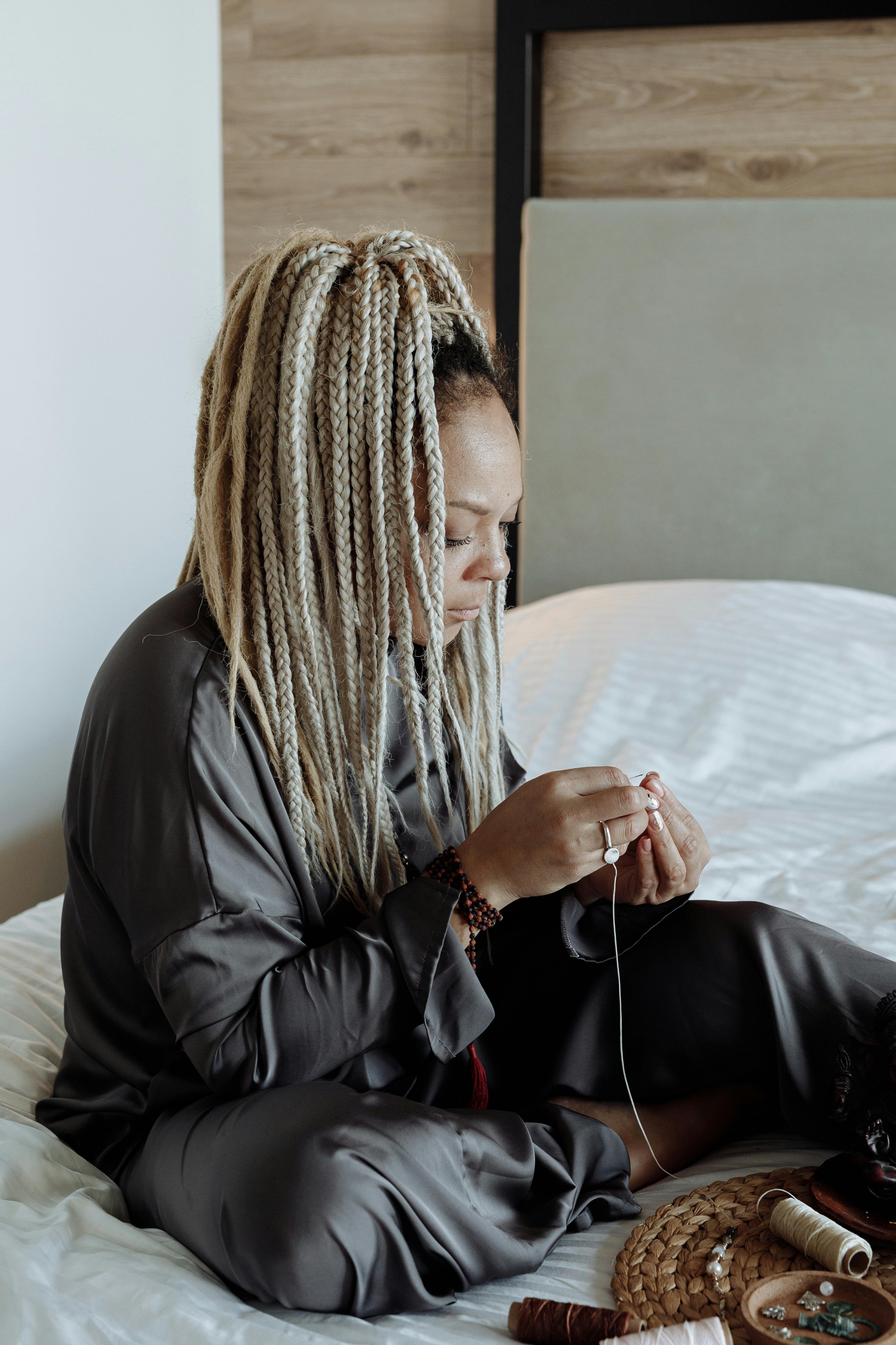 A Woman Sitting on Bed Holding a Thread · Free Stock Photo