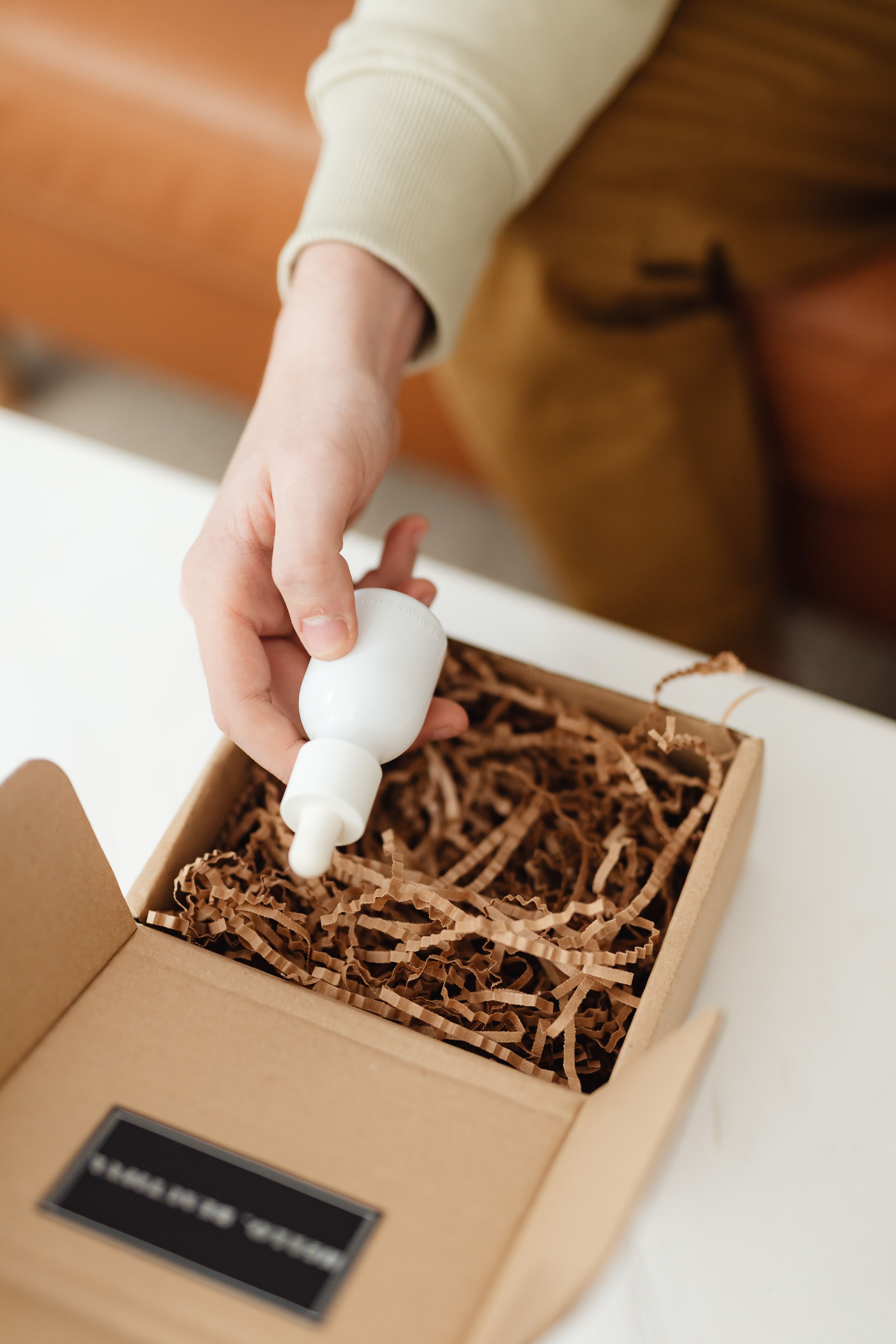 Hands of a Person Opening a Box with a White Bottle · Free Stock Photo