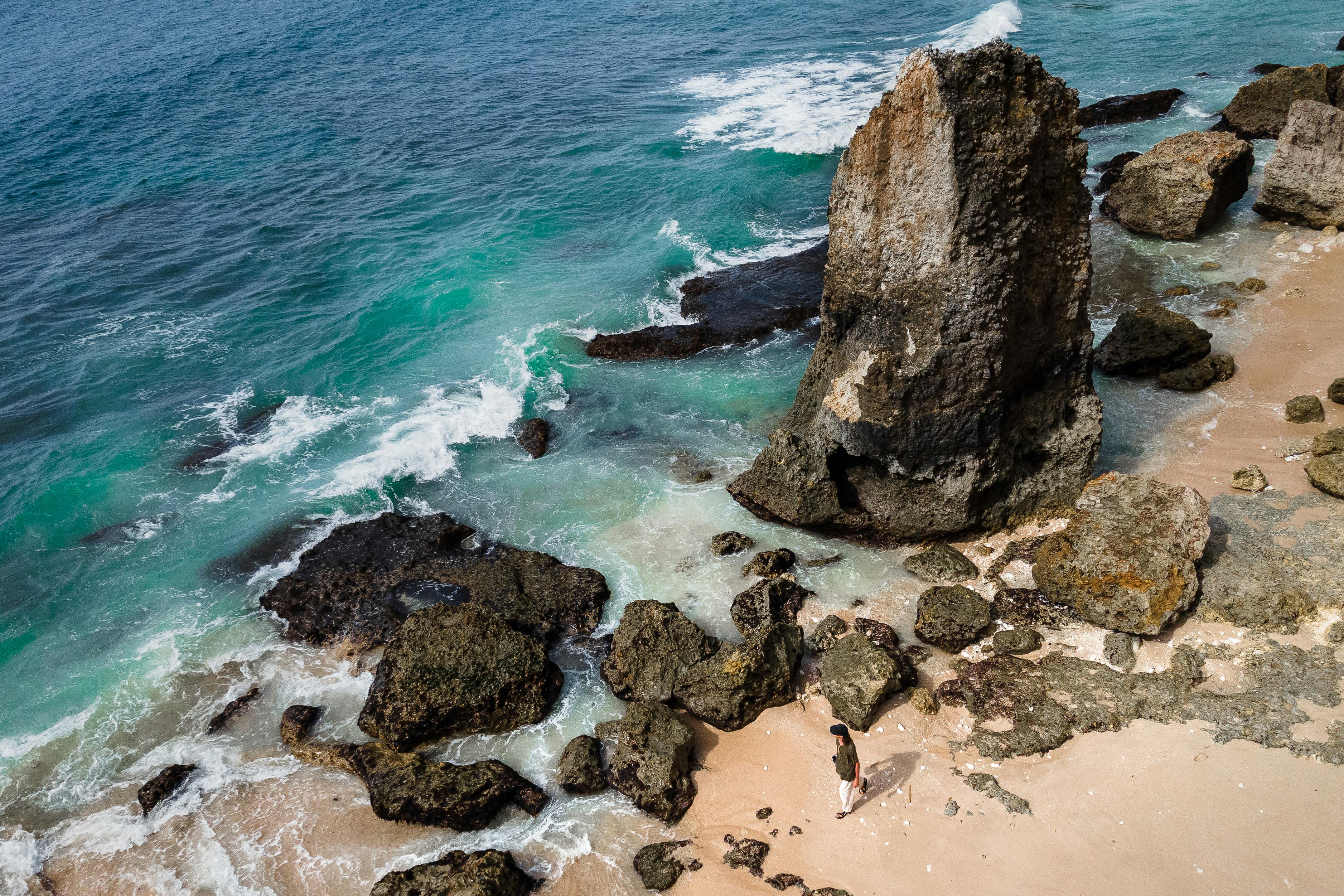 An Aerial Photography of a Person Walking on the Beach with Rock ...