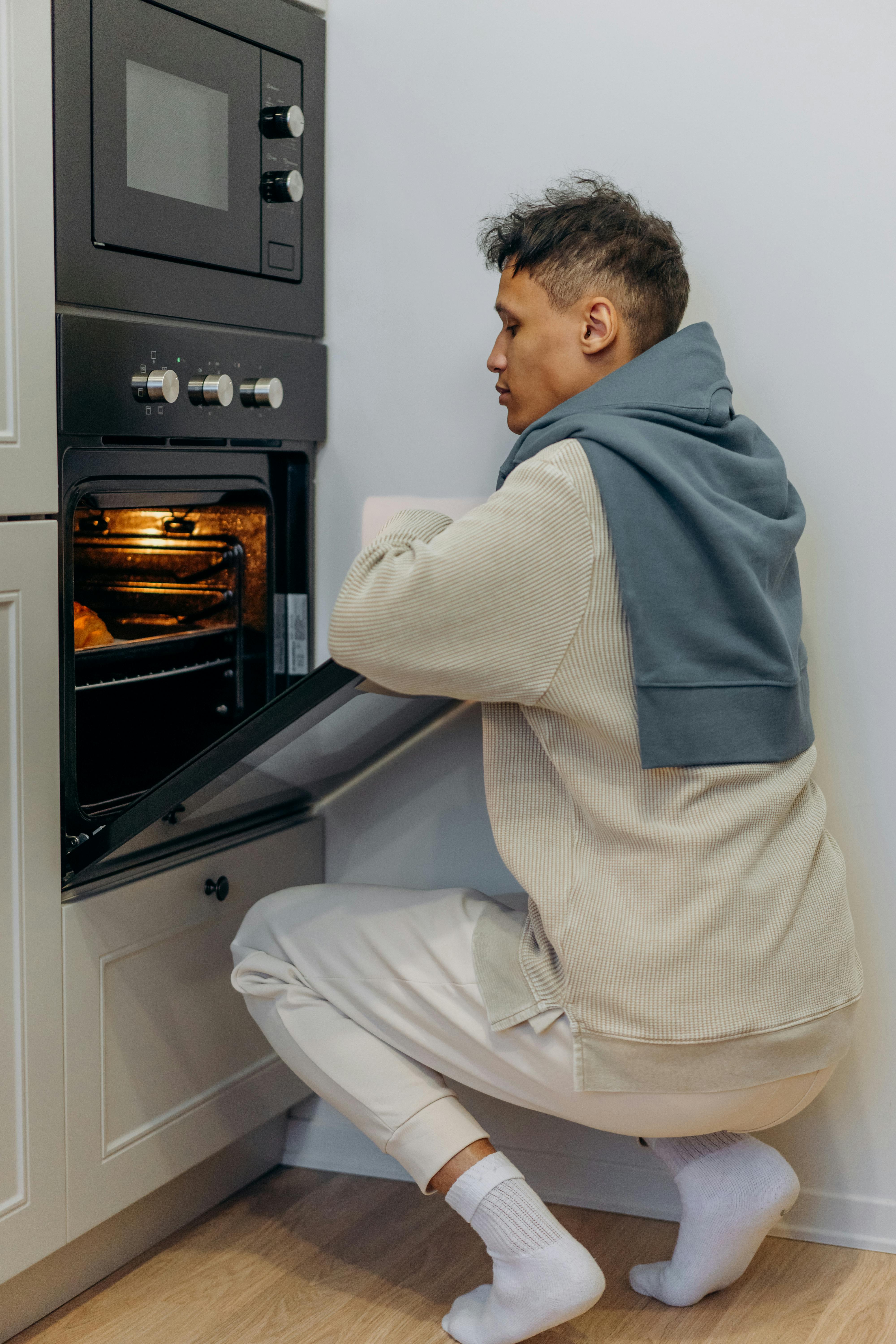 A Man with Sweater on Shoulders Looking Inside an Oven · Free Stock Photo