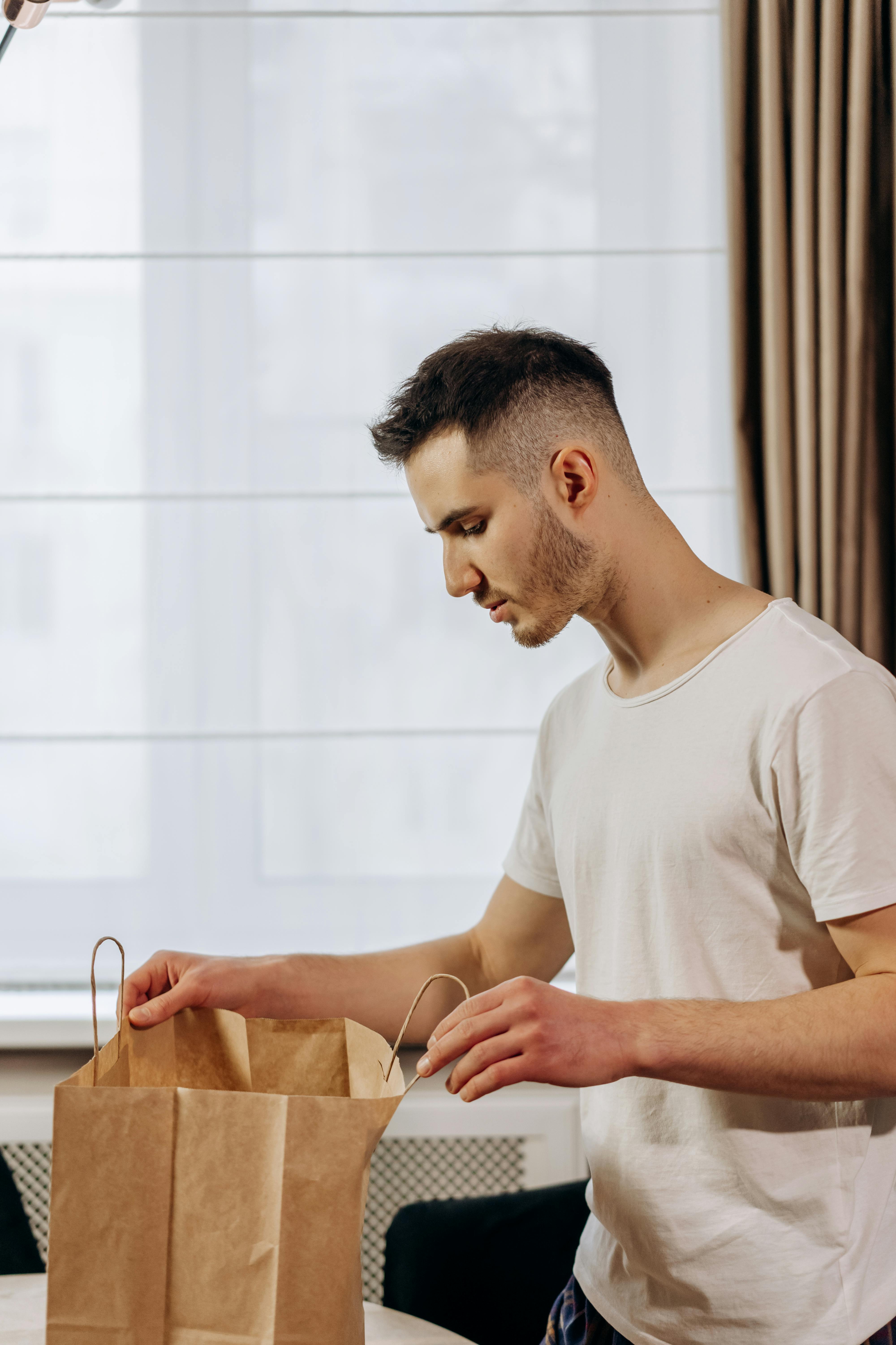 Man in White Crew Neck T-shirt Holding Brown Paper Bag · Free Stock Photo