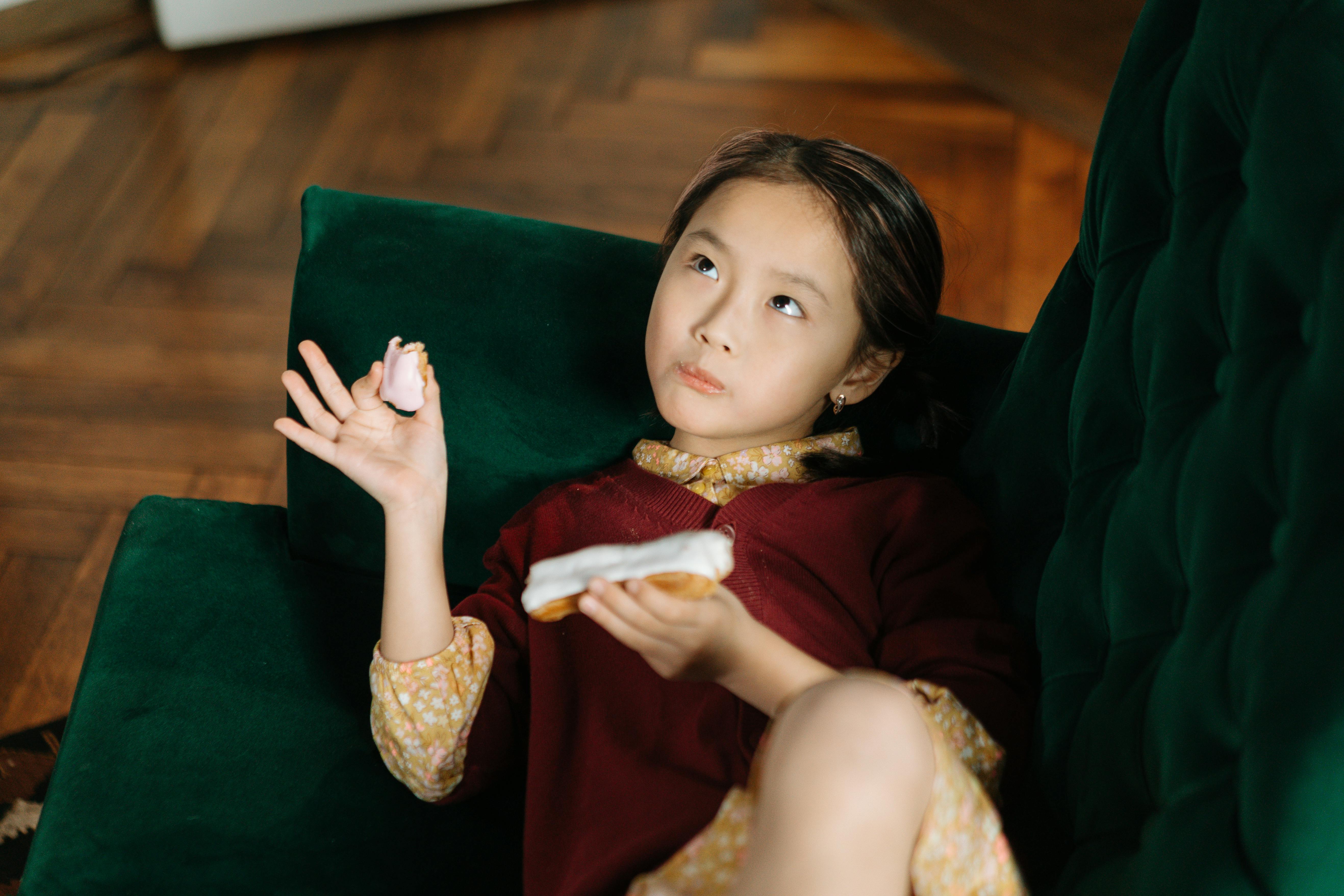 Girl Eating Icing Coated Bread While Sitting on a Green Couch · Free ...