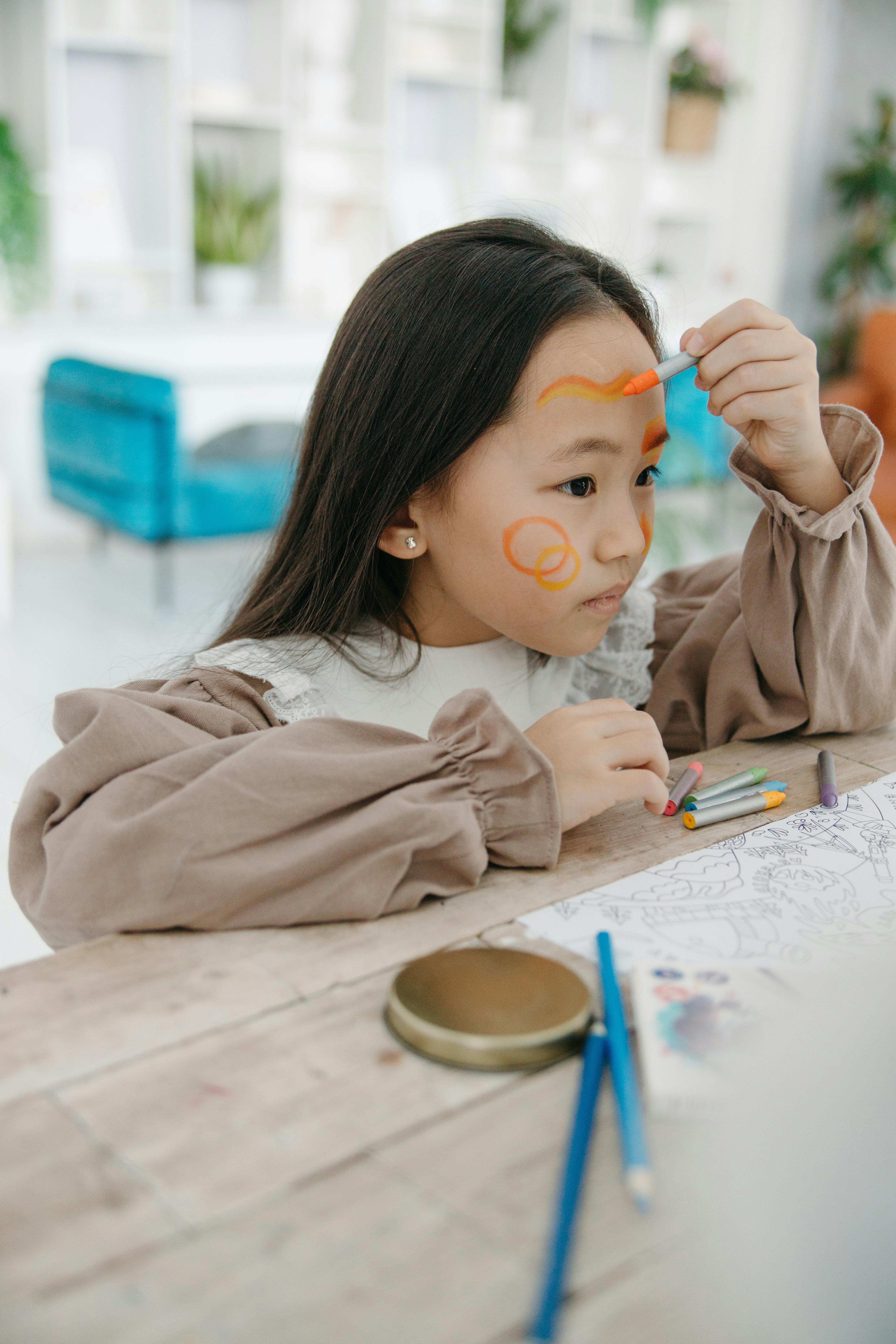 A Girl Drawing with Crayons on Face · Free Stock Photo