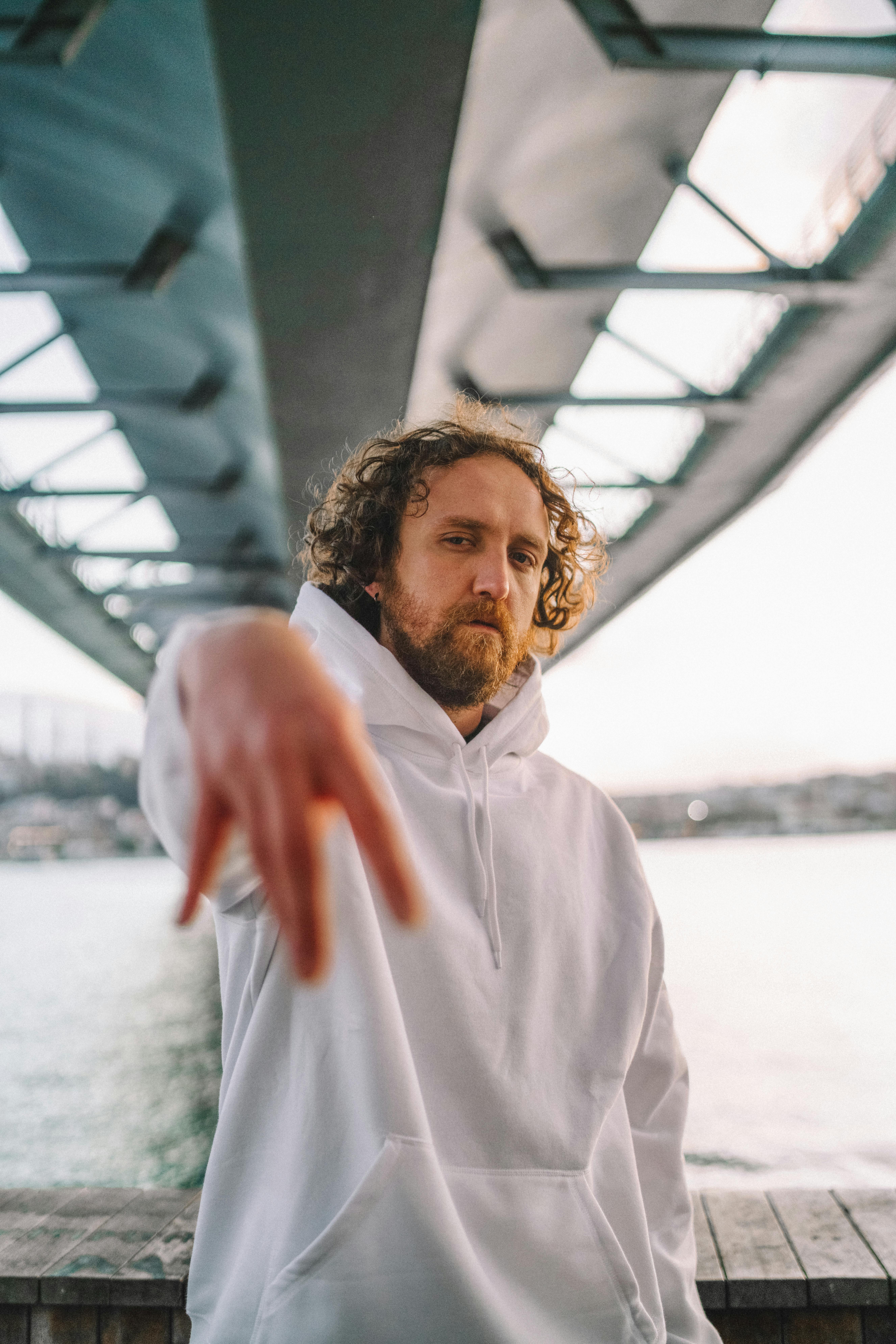 Man with fingers crossed gesture near river under bridge · Free Stock Photo