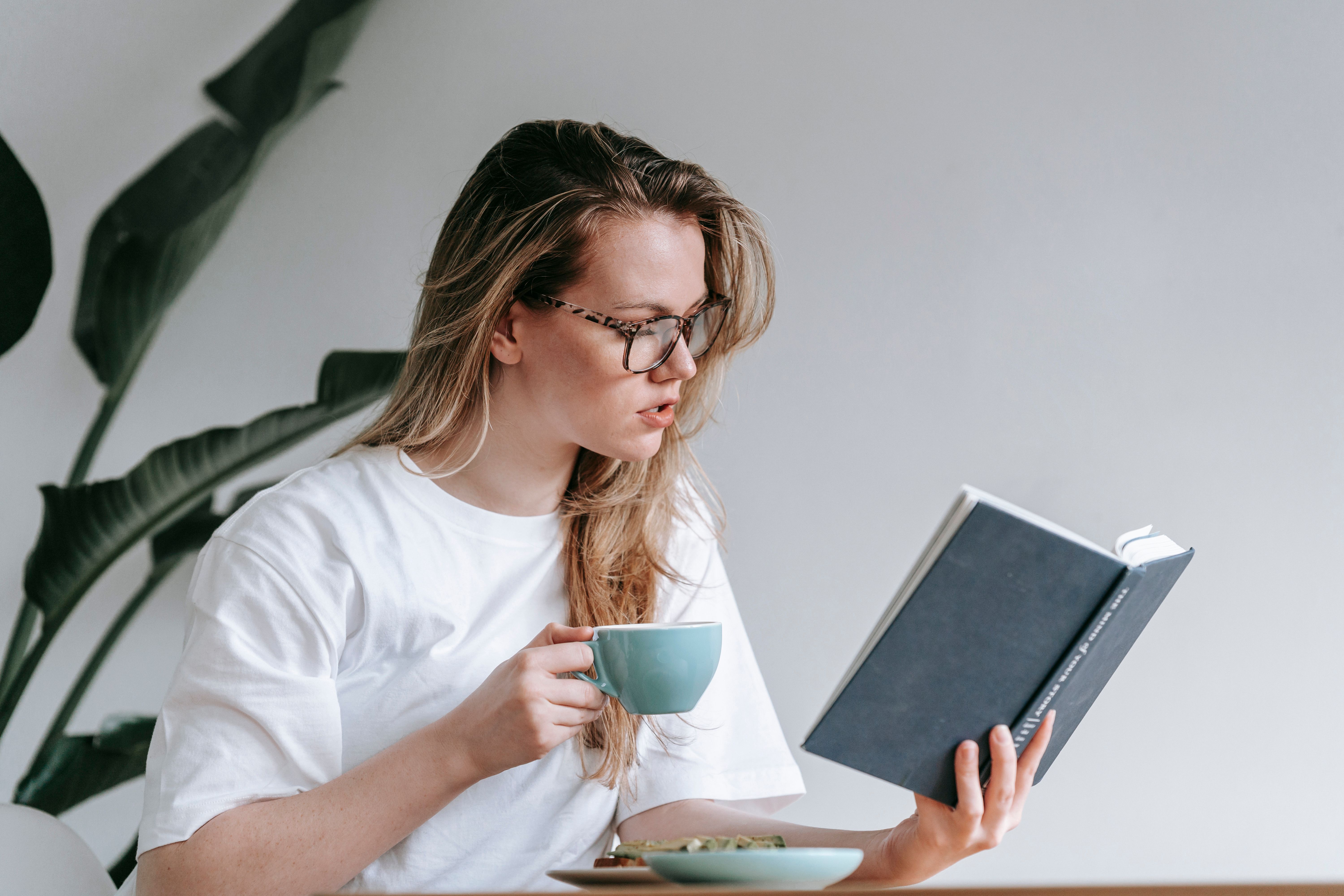 Serious woman with cup of fragrant coffee reading book · Free Stock Photo