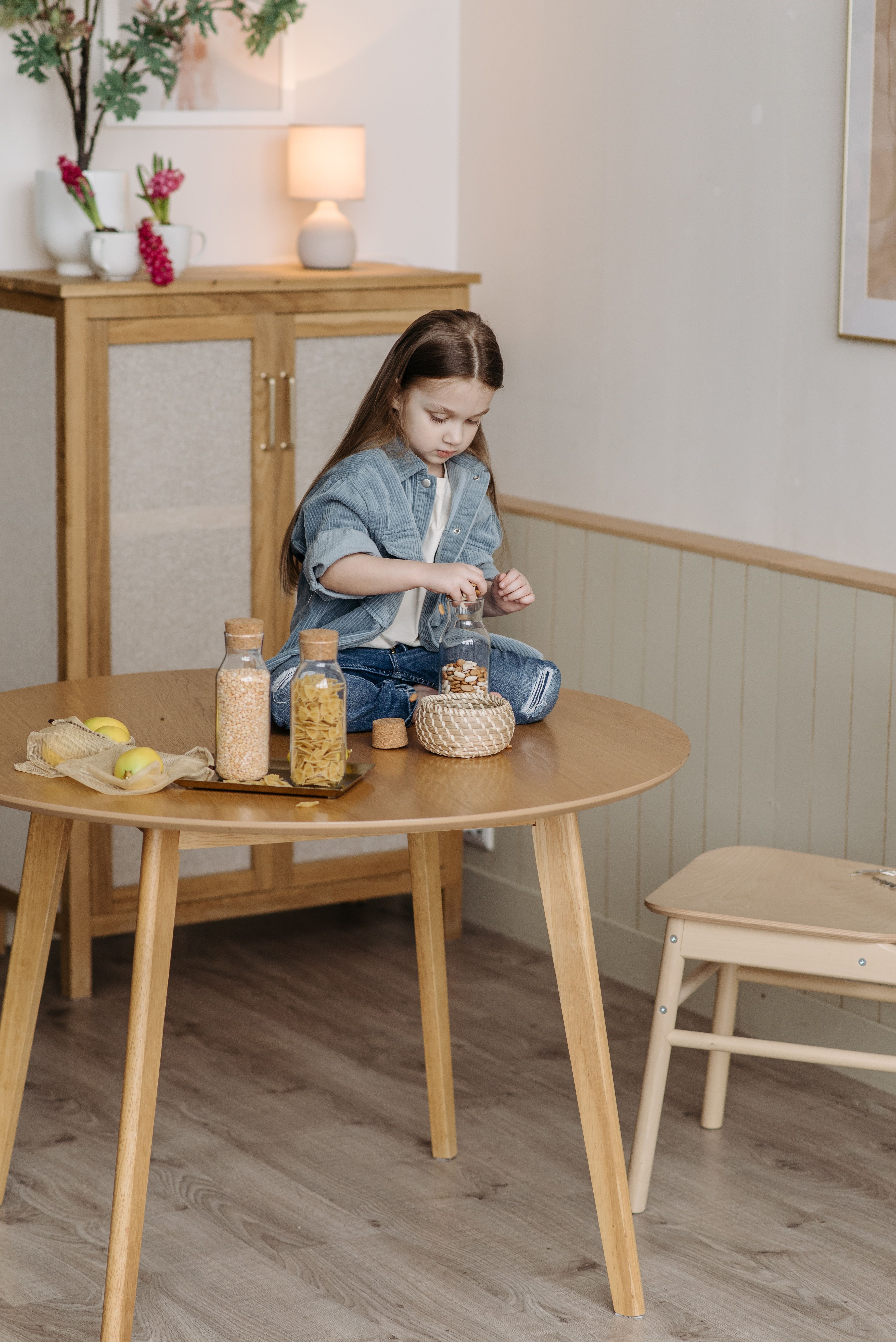 Girl Sitting on the Dining Table Filling Up Glass Containers · Free ...