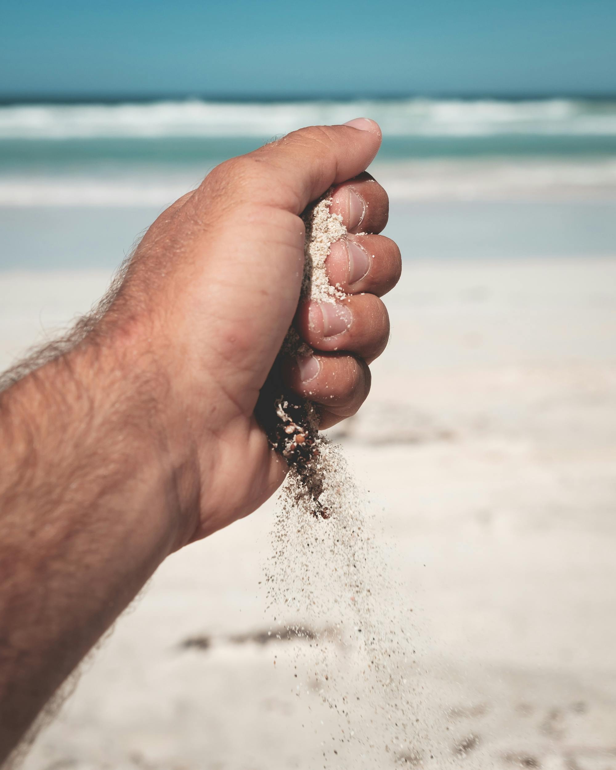 Man pouring sand from hand on beach of ocean · Free Stock Photo