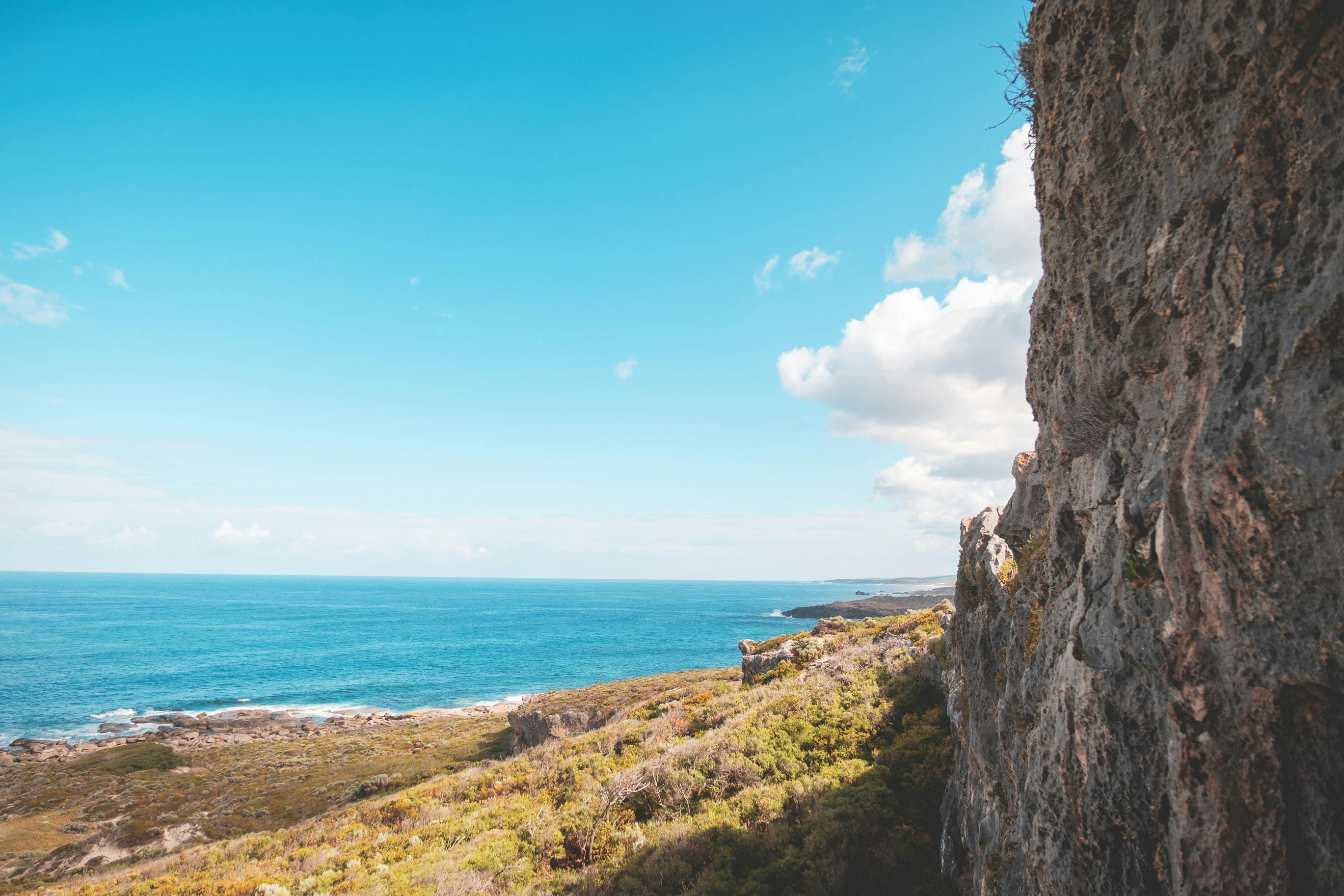 Shore with rocky cliff under cloudy blue sky · Free Stock Photo