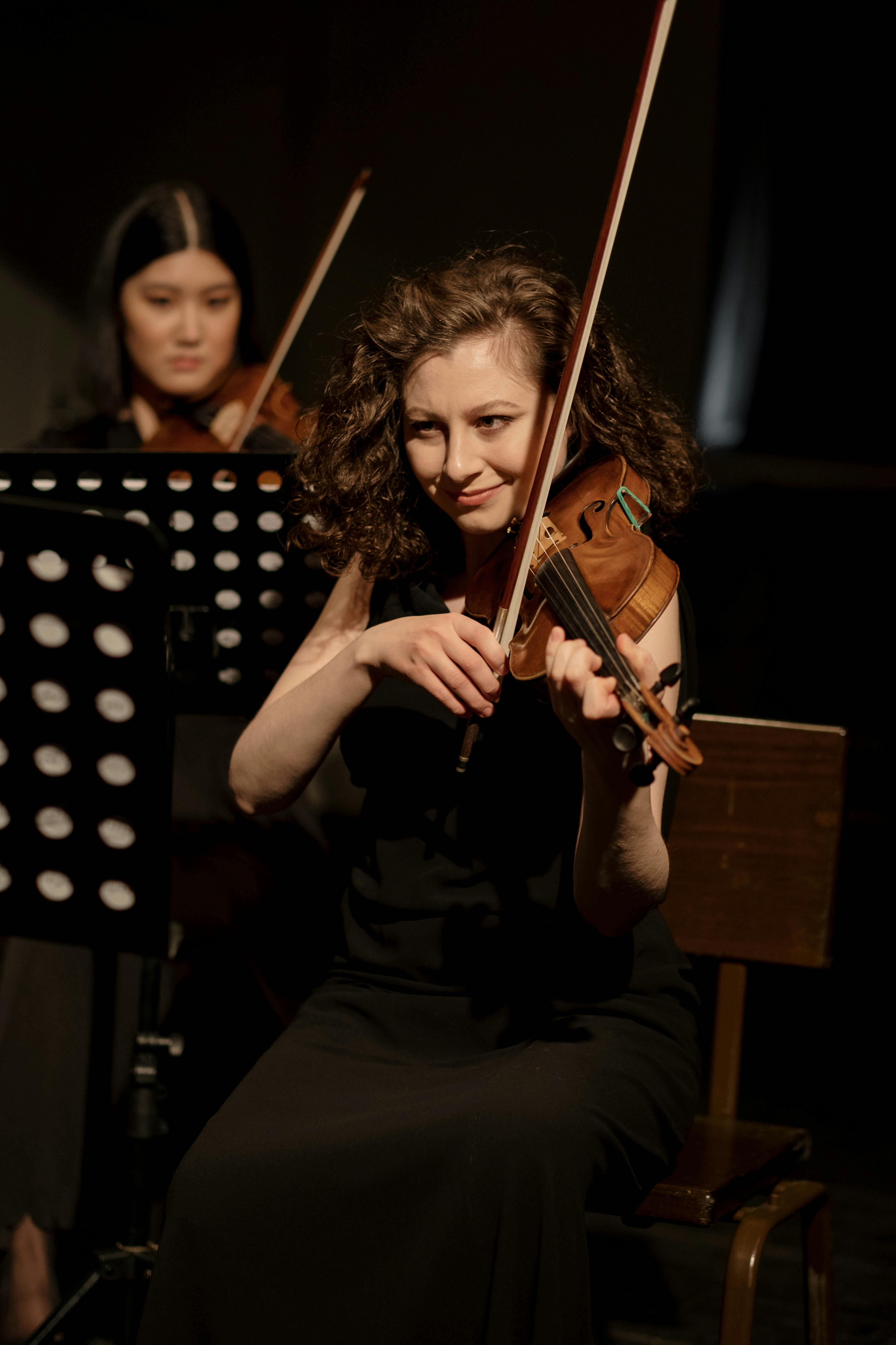 A Woman Sitting on a Wooden Chair while Playing Violin · Free Stock Photo