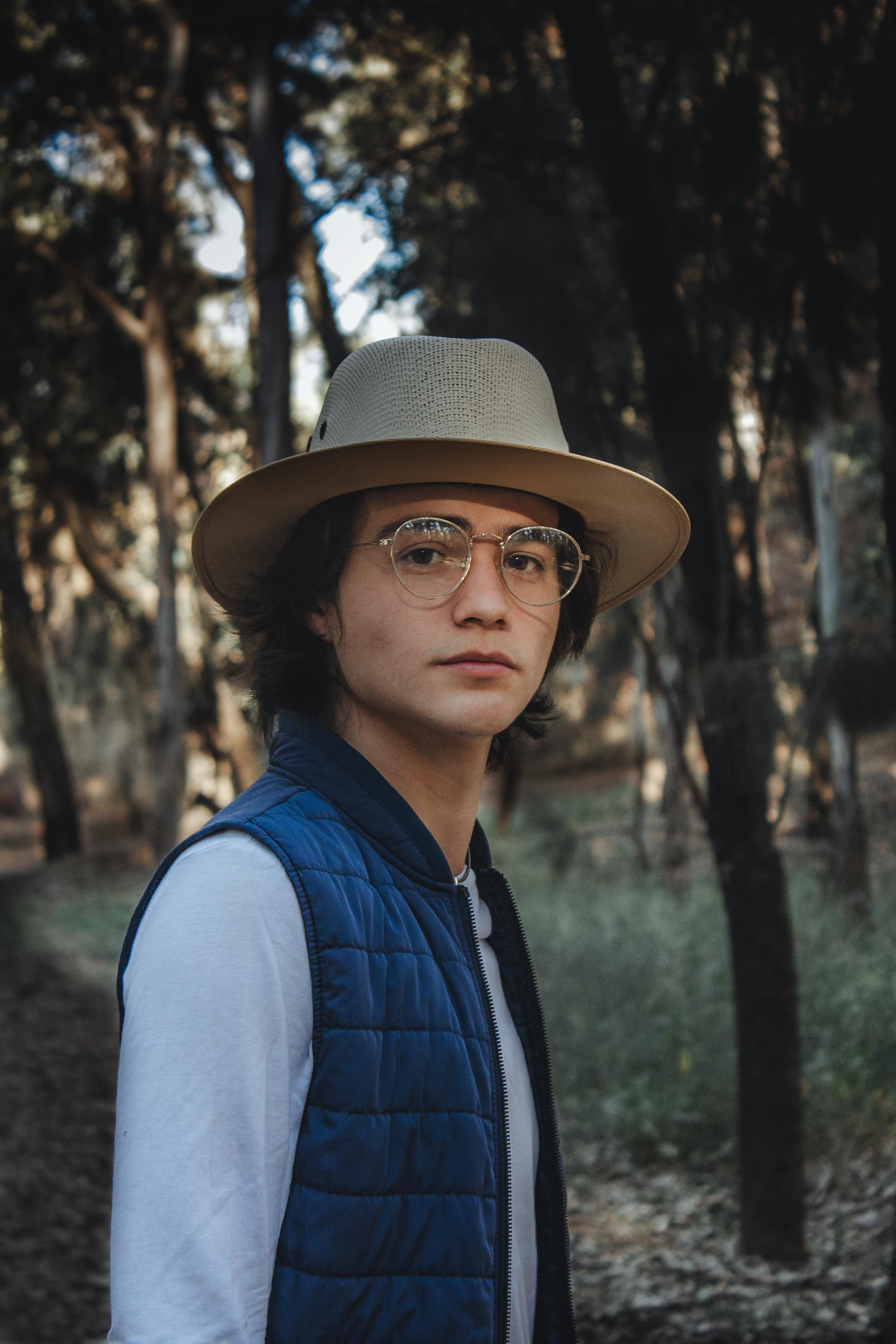 Joven Con Chaleco Azul Y Sombrero Marrón De Pie Cerca De árboles · Foto ...