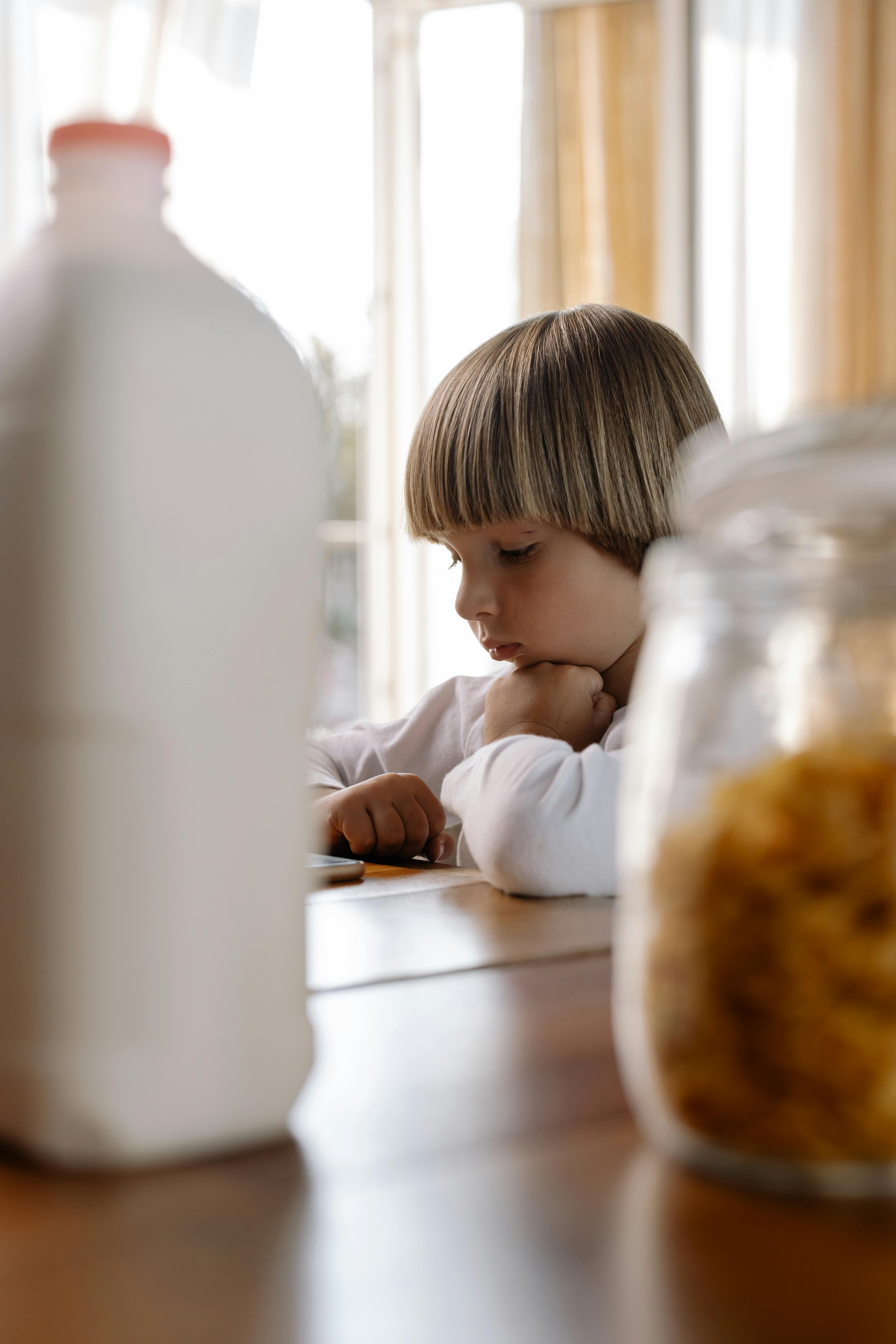 A Boy Sitting on and Looking Down on Wooden Table · Free Stock Photo