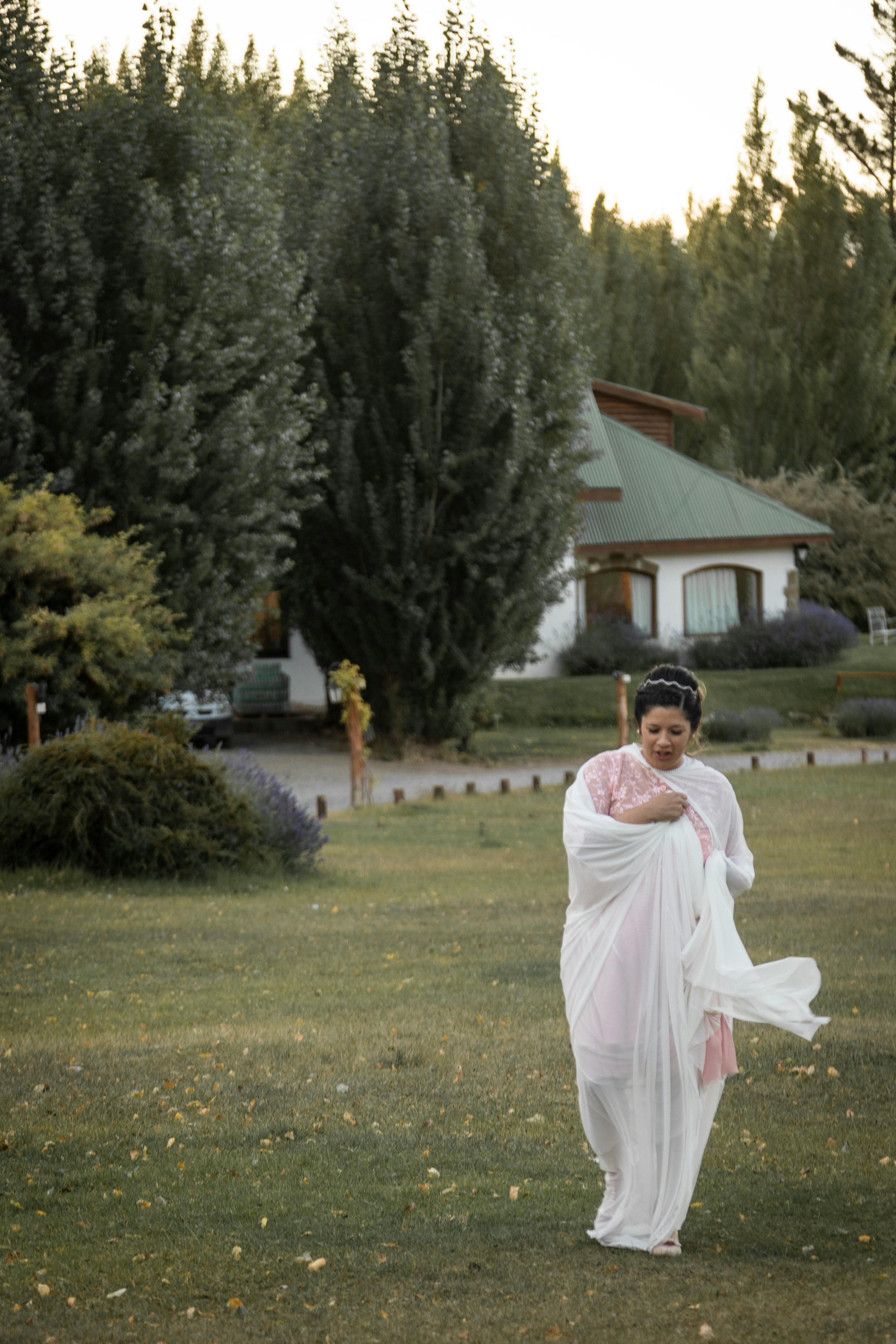 Woman Wearing a White Gown Walking on Grass Field · Free Stock Photo