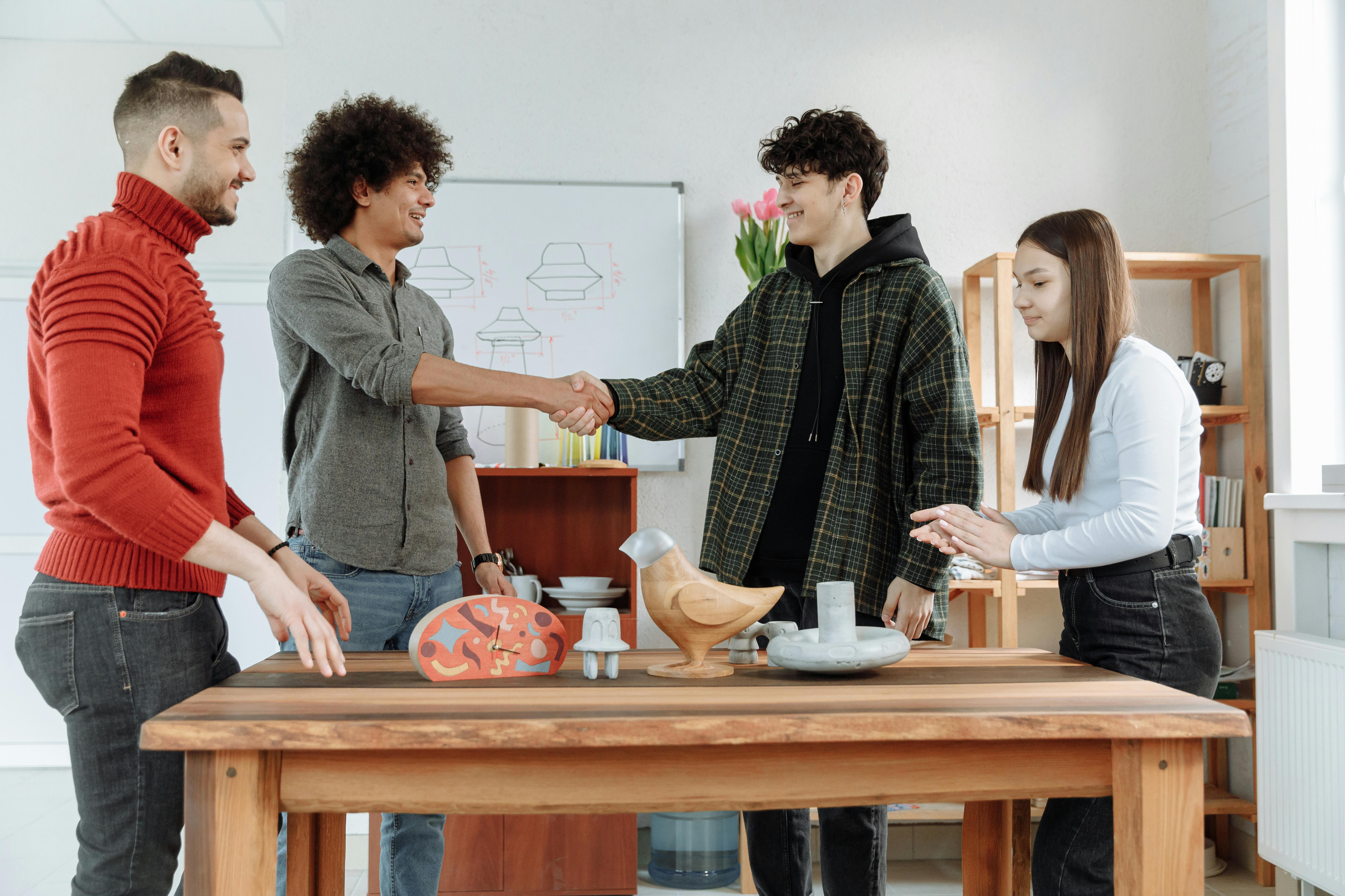 Two Men Making a Hand Shake Beside a Table with Artworks · Free Stock Photo