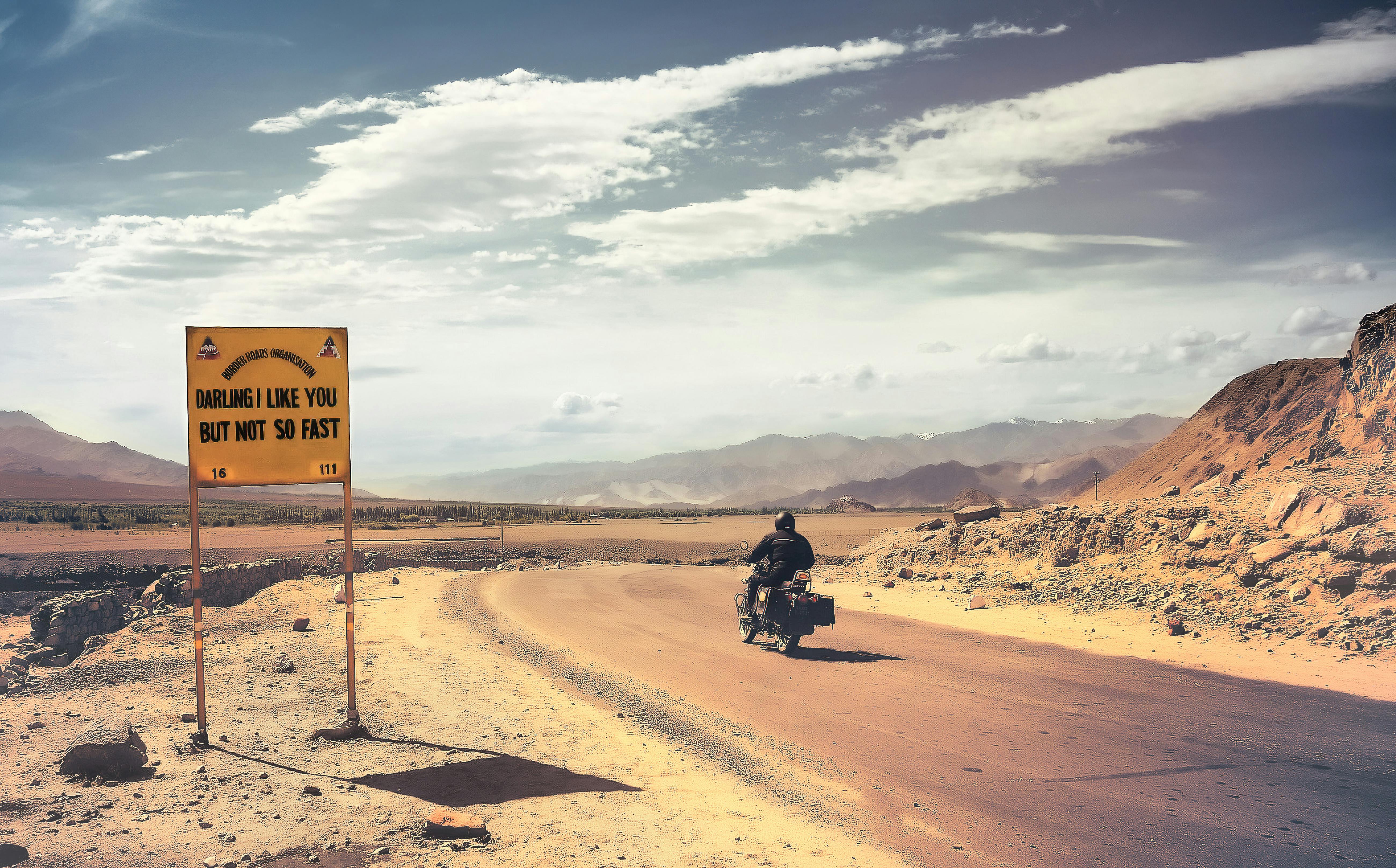 Man Riding a Motorcycle and a Humorous Road Sign · Free Stock Photo