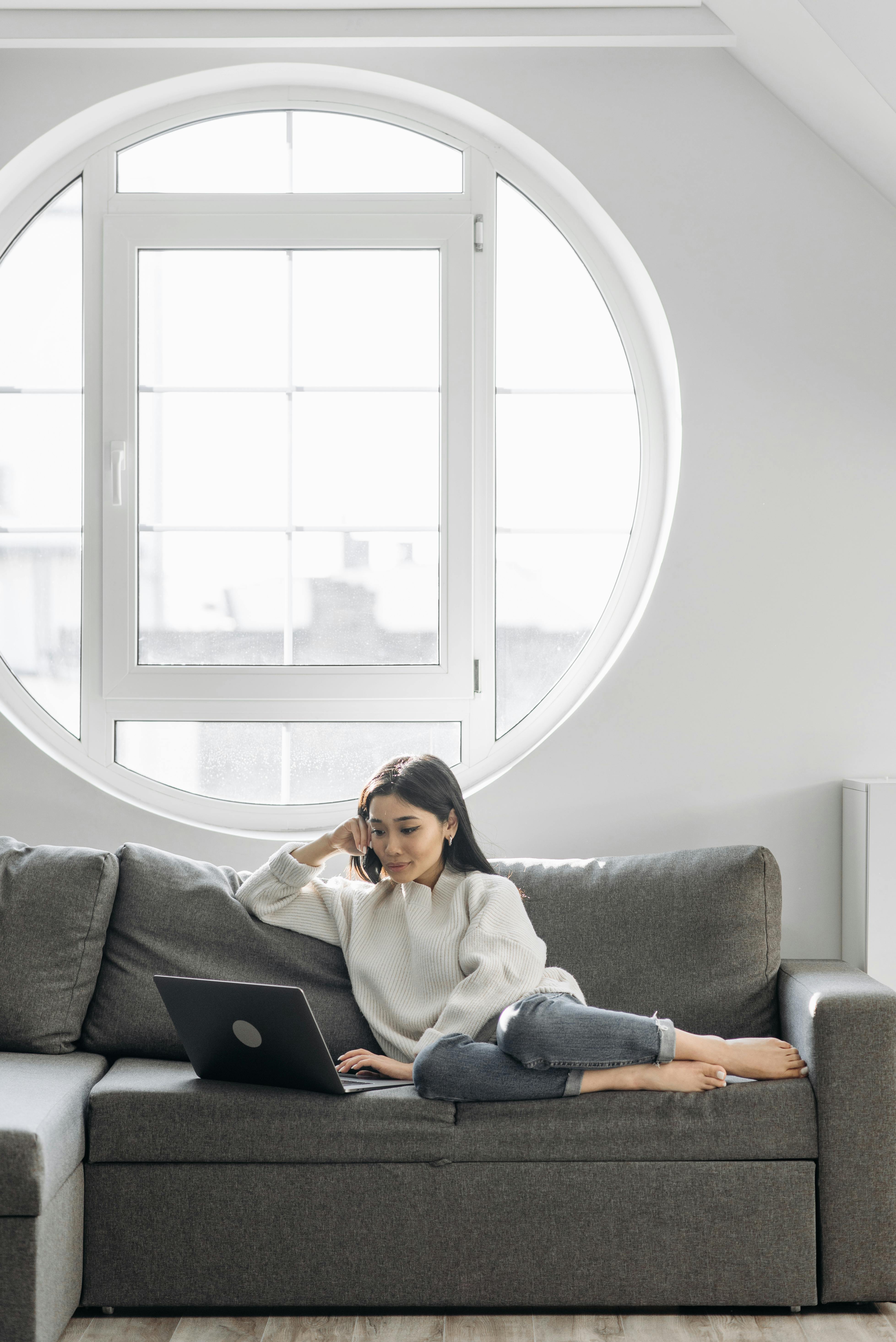 A Woman Sitting on the Couch while Using Her Laptop · Free Stock Photo