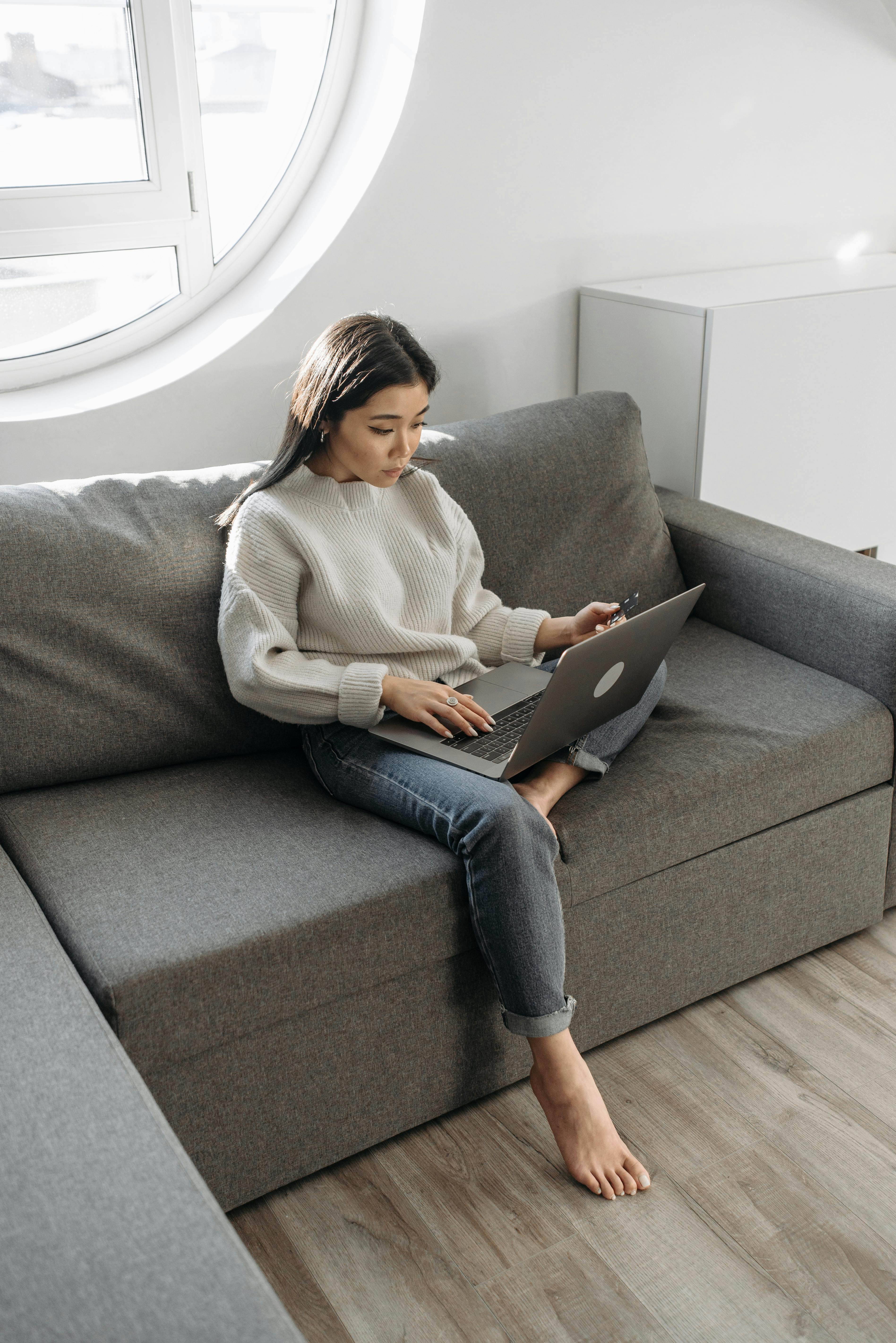 A Woman Sitting on the Couch while Using Her Laptop · Free Stock Photo