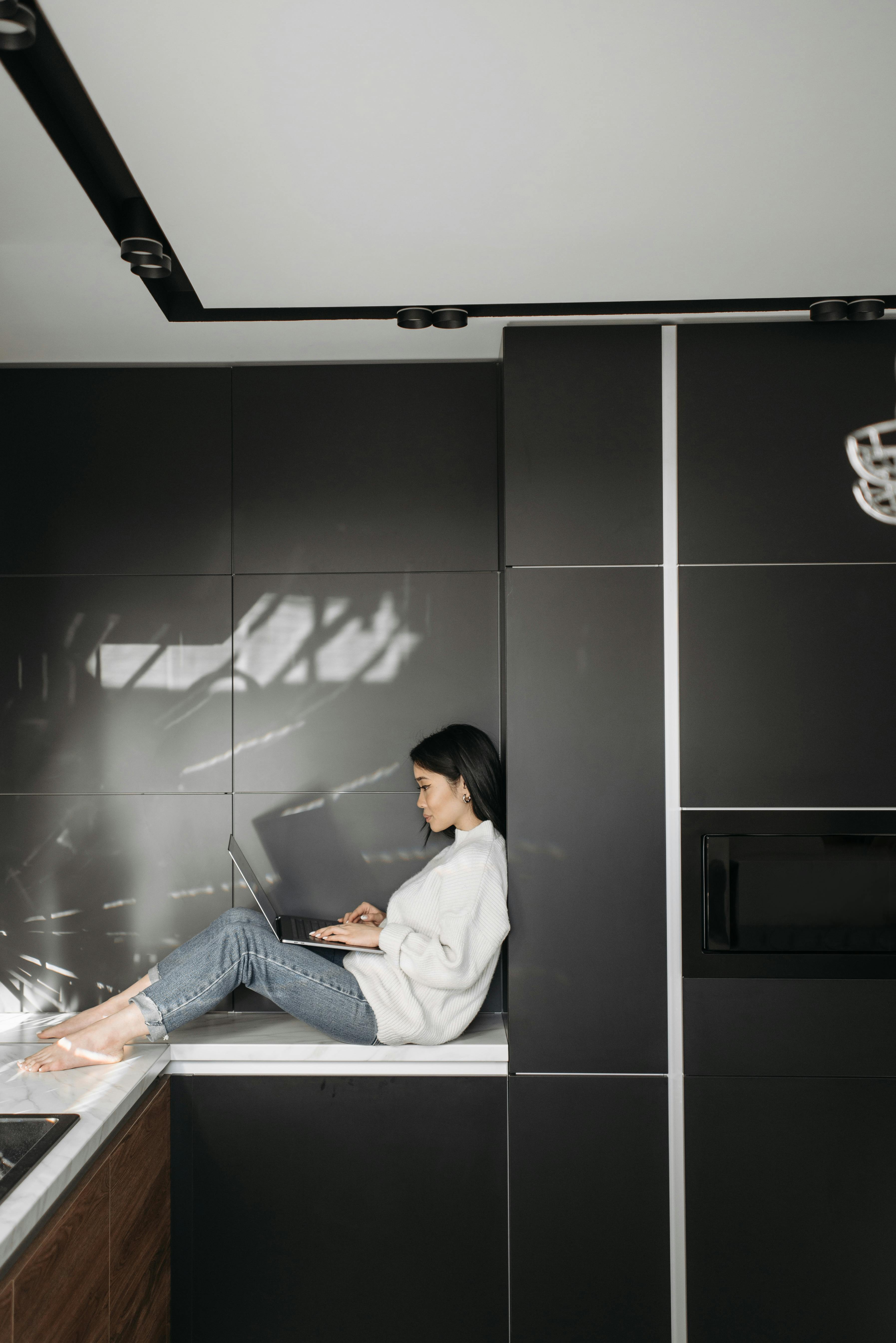 Woman Sitting on White Counter Top while Using Laptop · Free Stock Photo