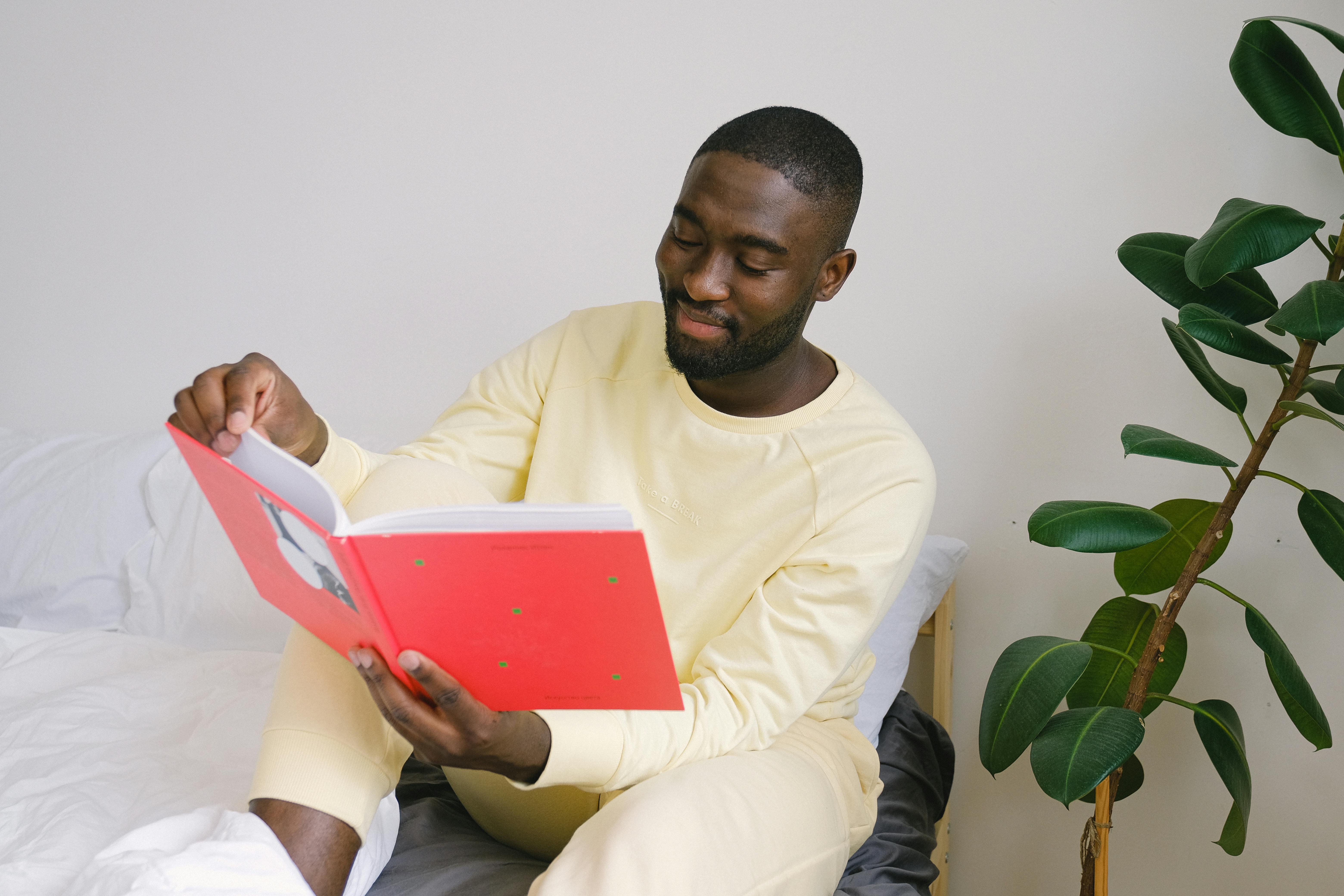 Man Reading a Book while Sitting on the Bed · Free Stock Photo