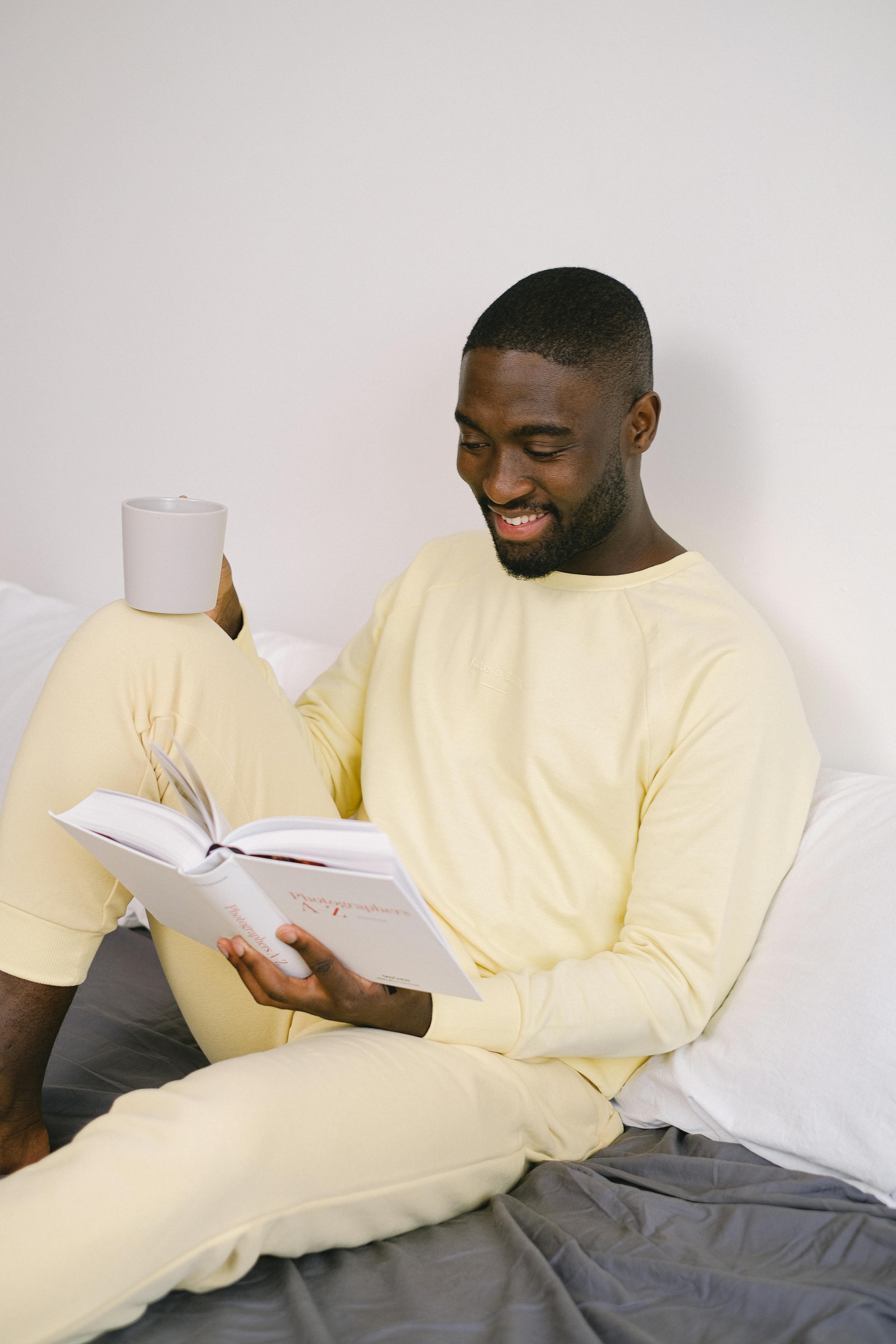 A Man Reading Book while Sitting on a Bed · Free Stock Photo