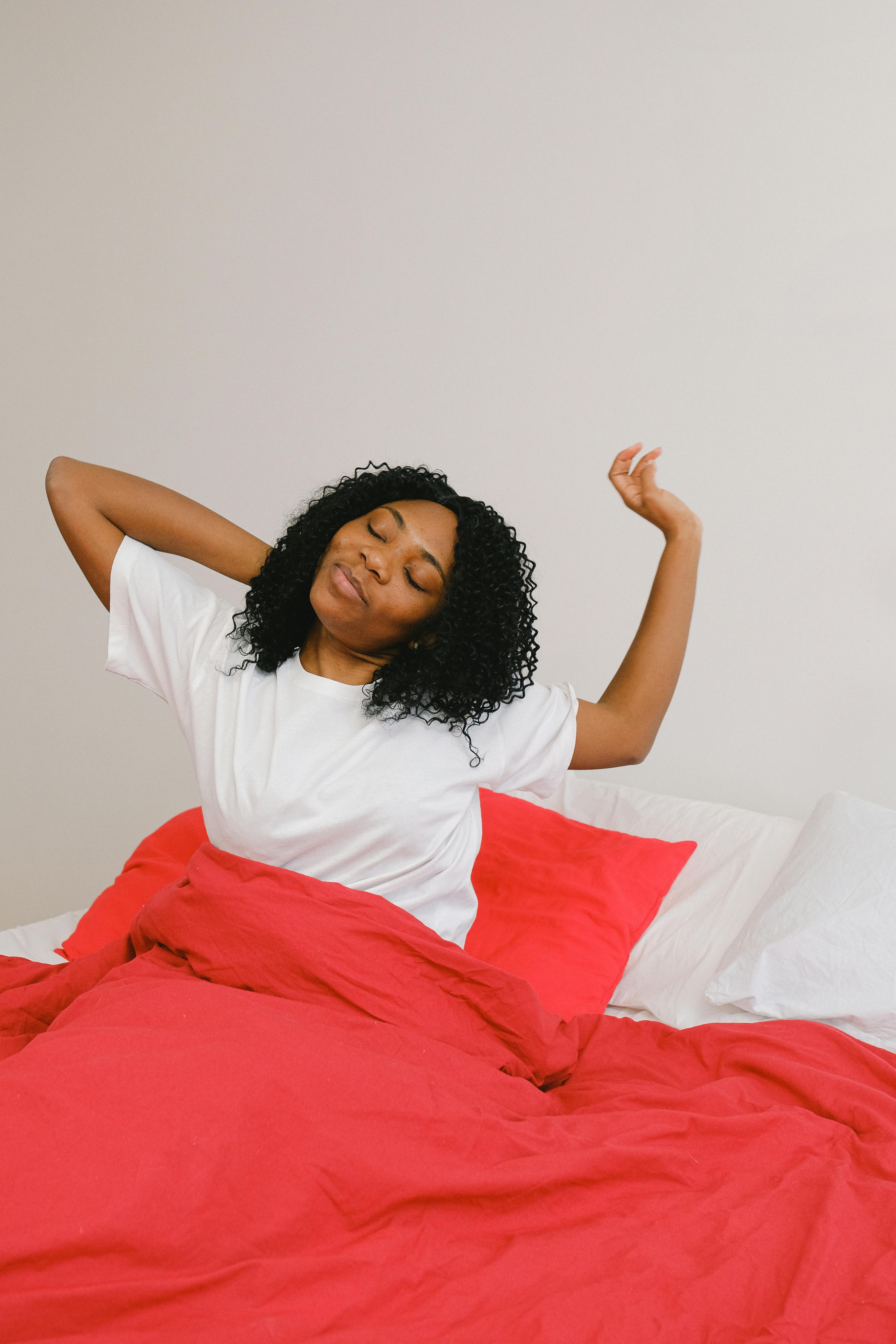 Cheerful black woman waking up in bed with red blanket · Free Stock Photo