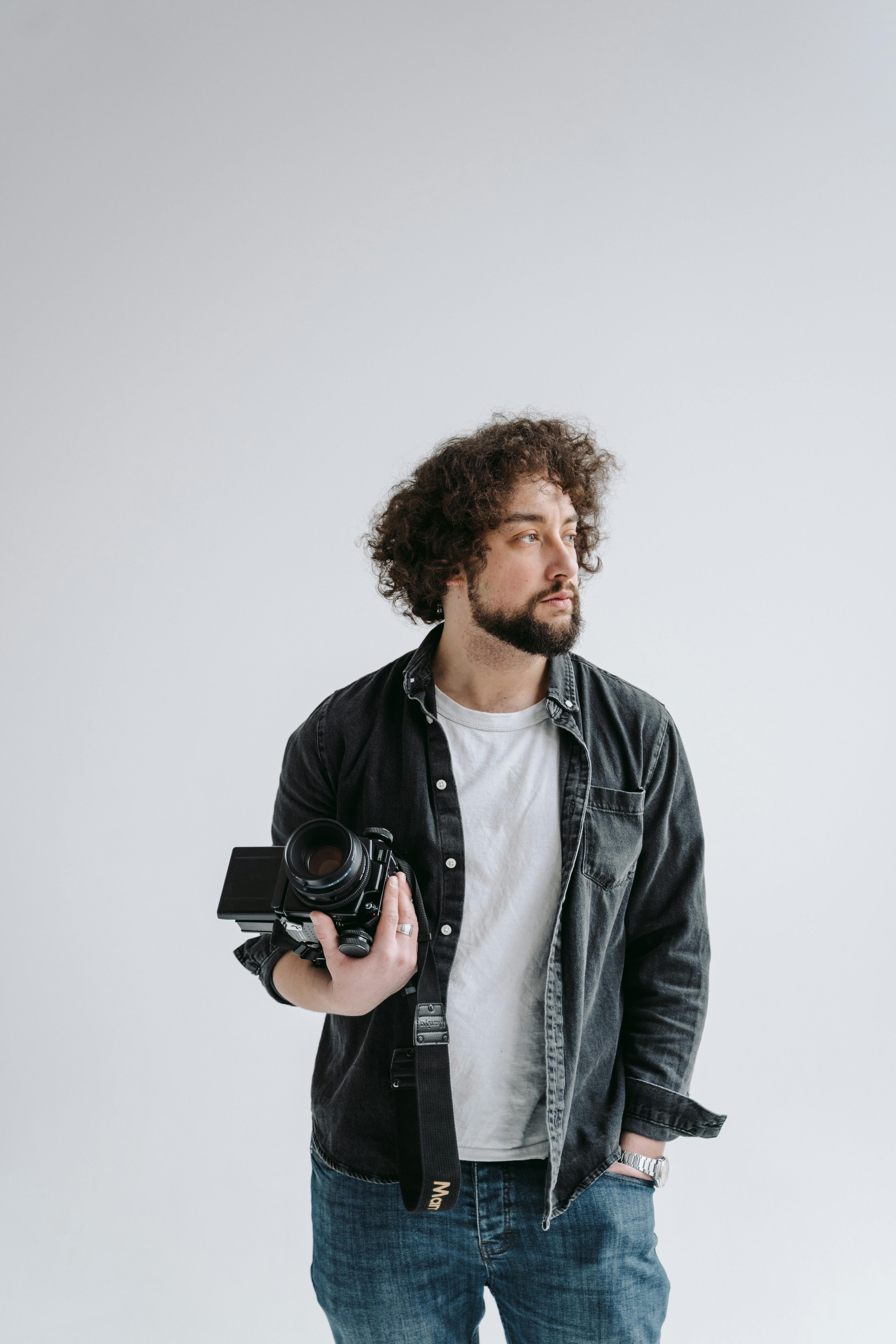Man Looking Afar While Holding a Black Dslr Camera · Free Stock Photo