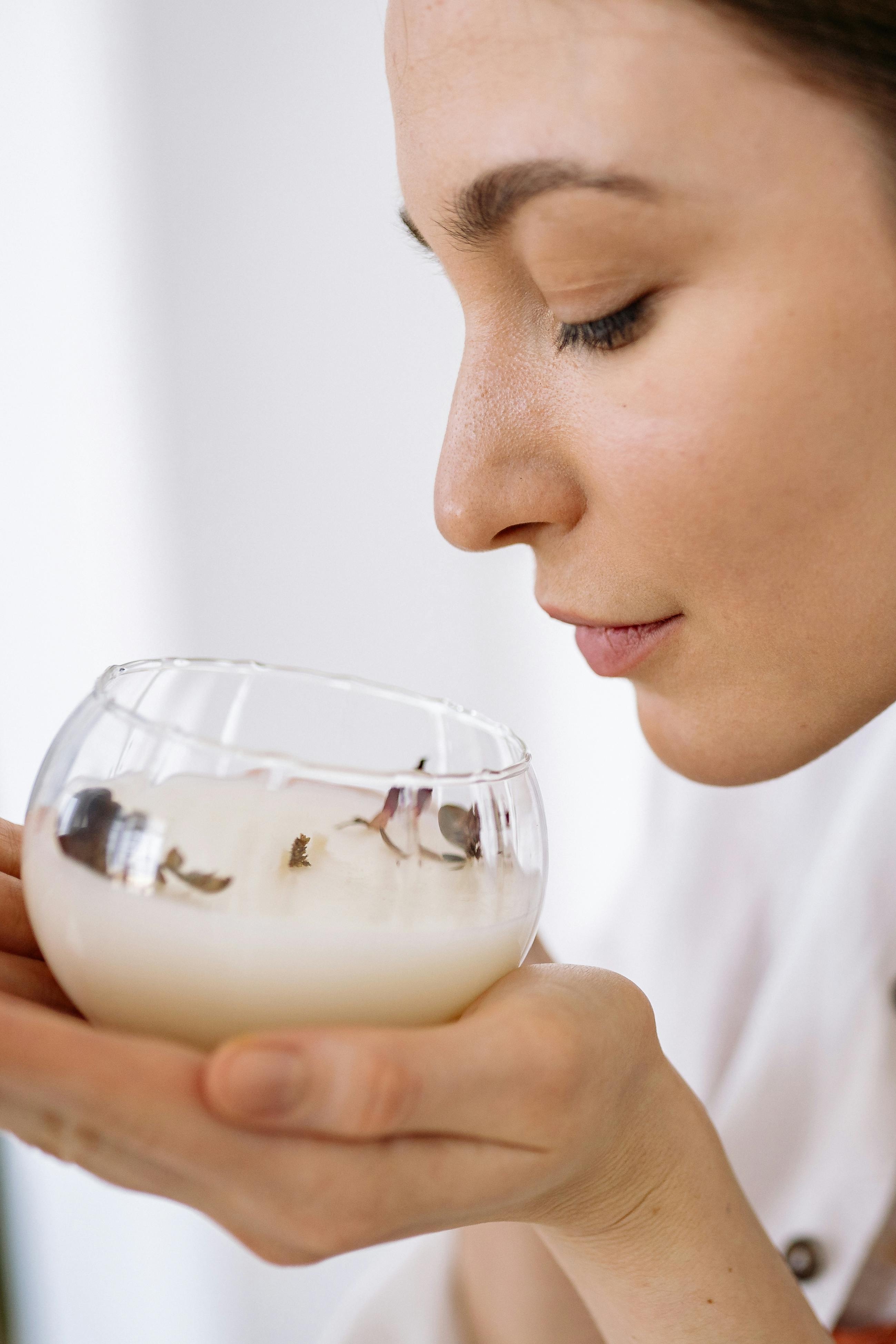 A Woman Smelling the Fragrance of a Candle on a Clear Glass Container ...