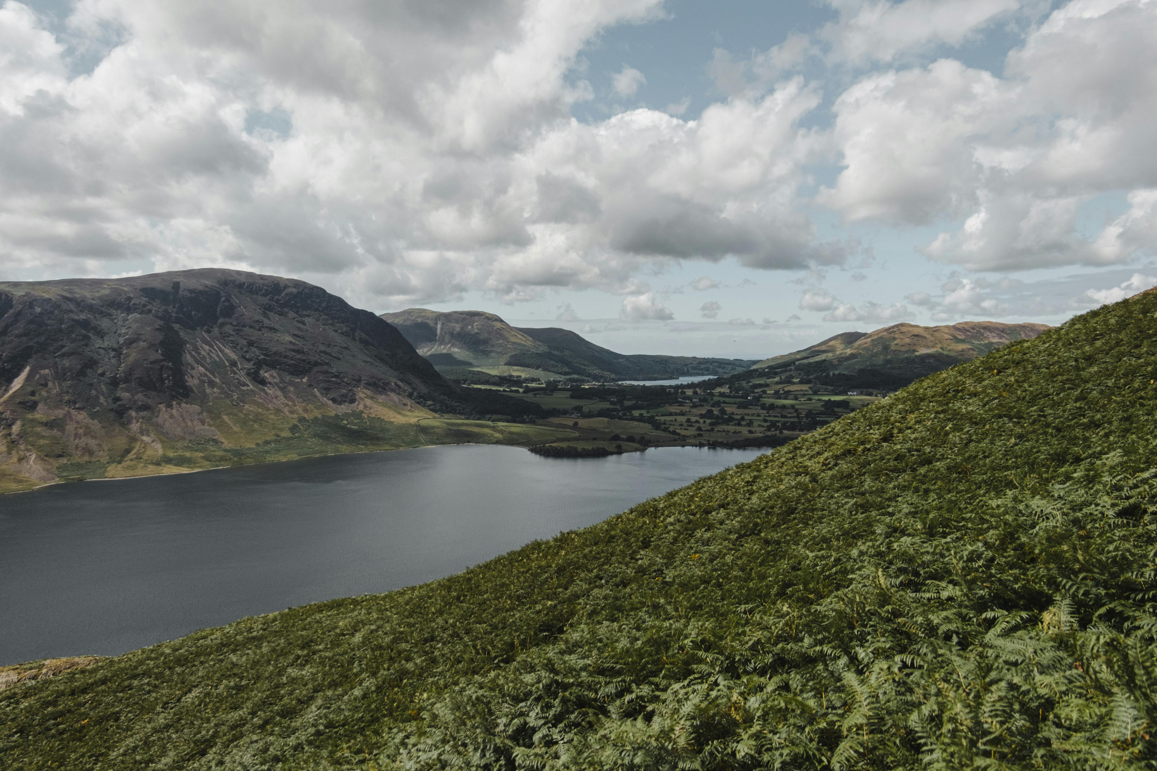 Grassy slope near river and mountains · Free Stock Photo