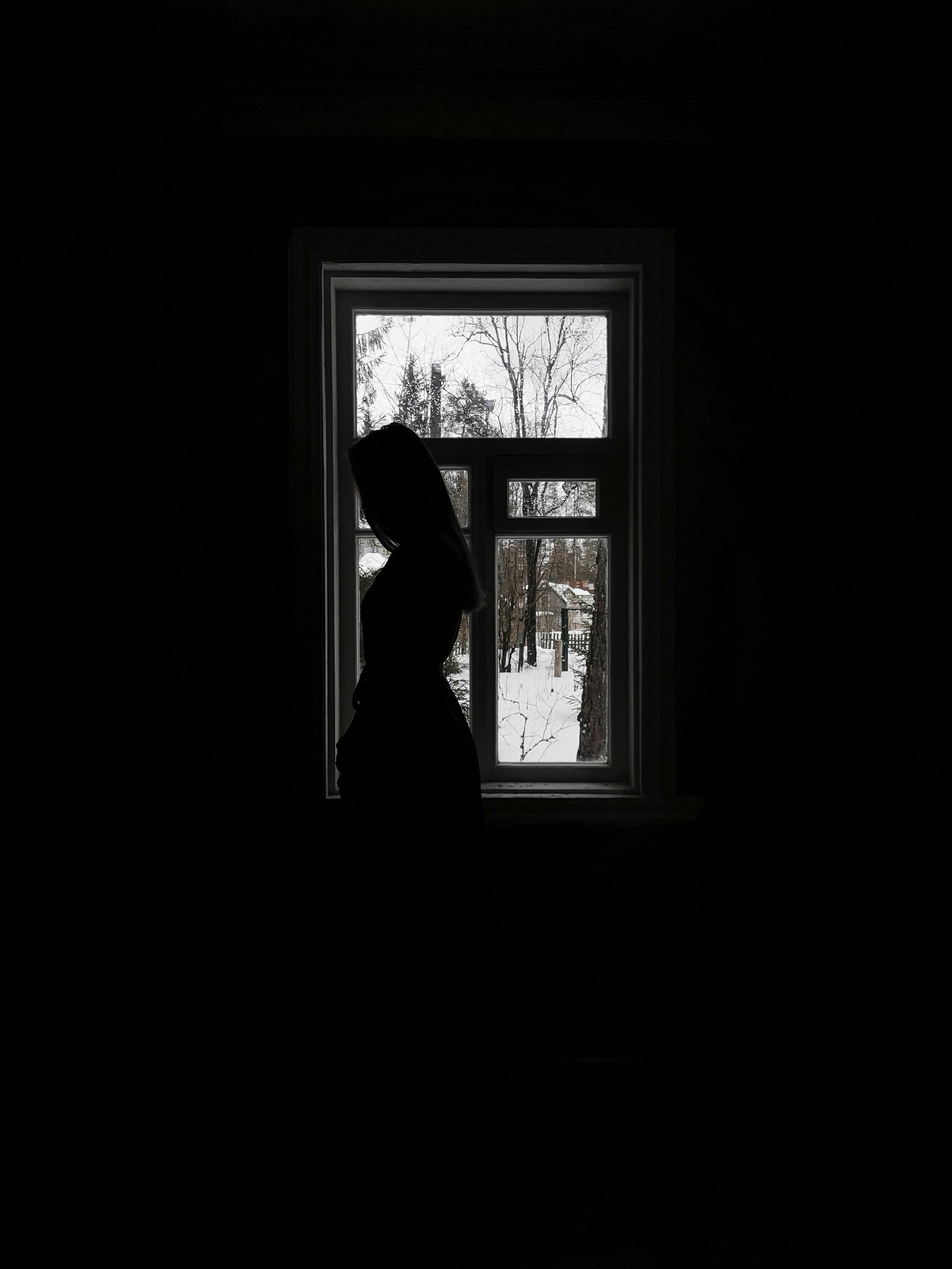 Pensive female standing near window in dark room · Free Stock Photo