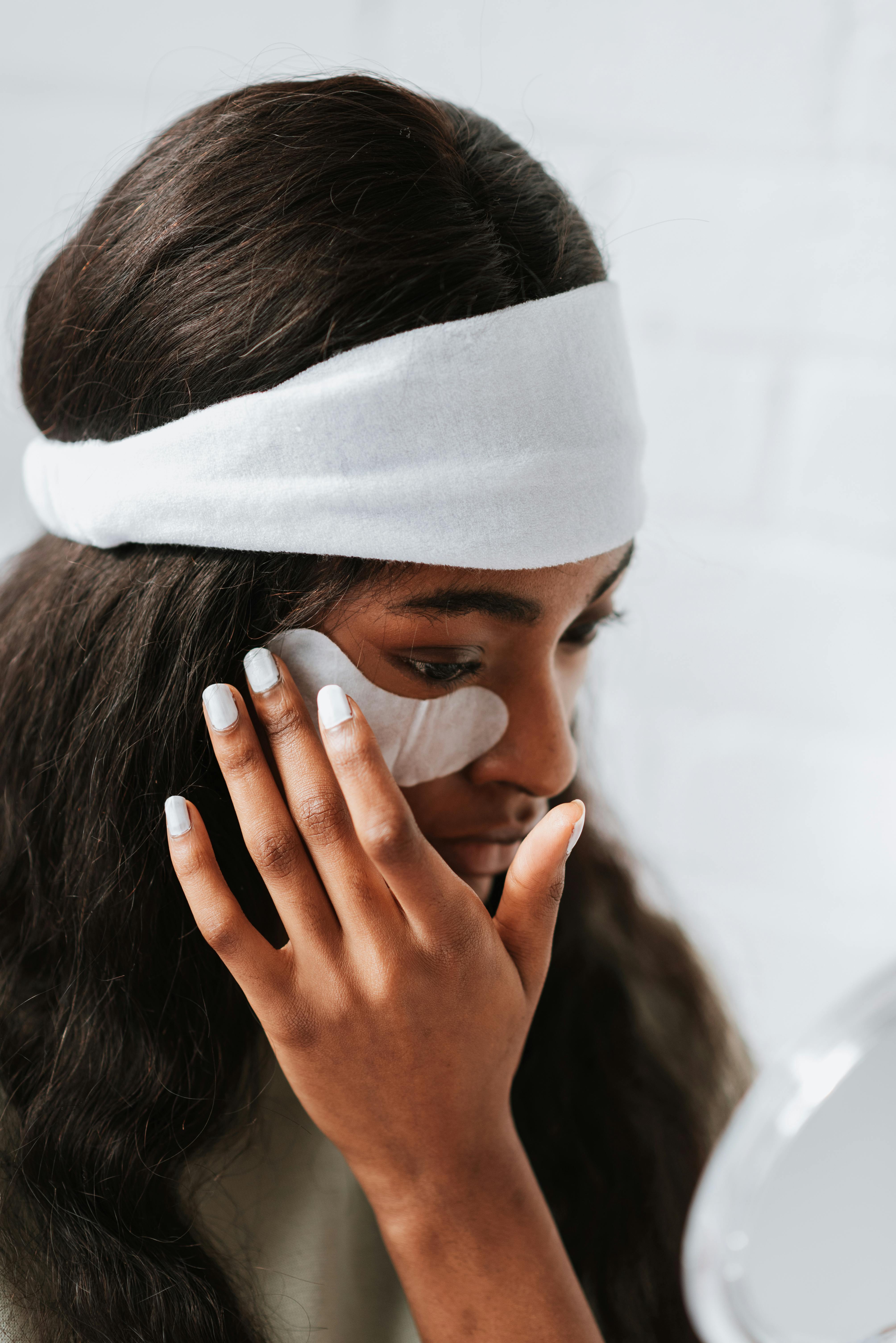 Ethnic woman applying eye patch on cheek · Free Stock Photo