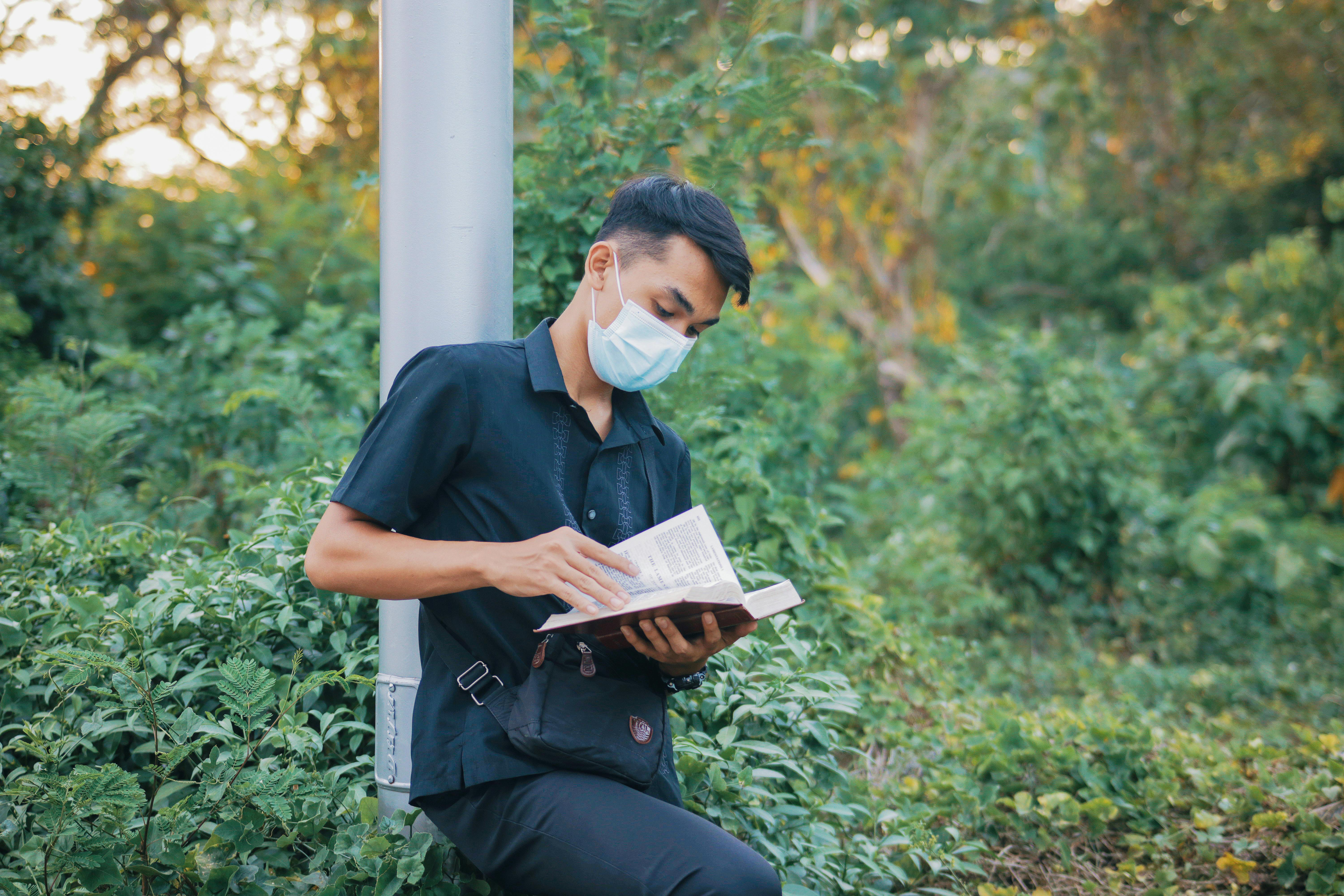 A Man in a Face Mask Reading a Book by a Lamppost · Free Stock Photo